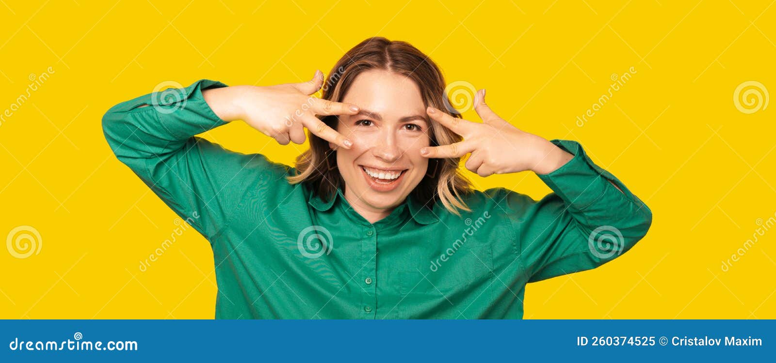 Playful Blonde Woman Is Showing V Gesture With Both Hands Near Her Face