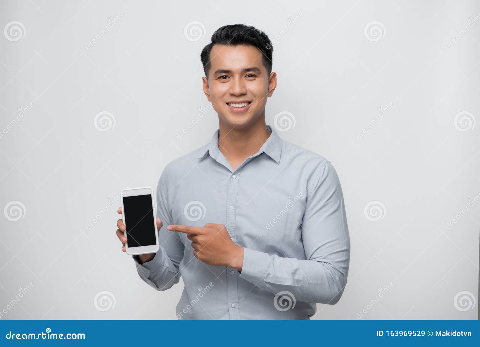 Pleased Happy Young Asian Man Holding Smartphone Pointing At Cellphone