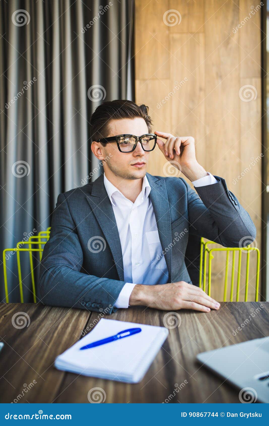 Portrait Of Attractive Young Man In Glasses Sitting At Office Desk With Laptop Computer Stock