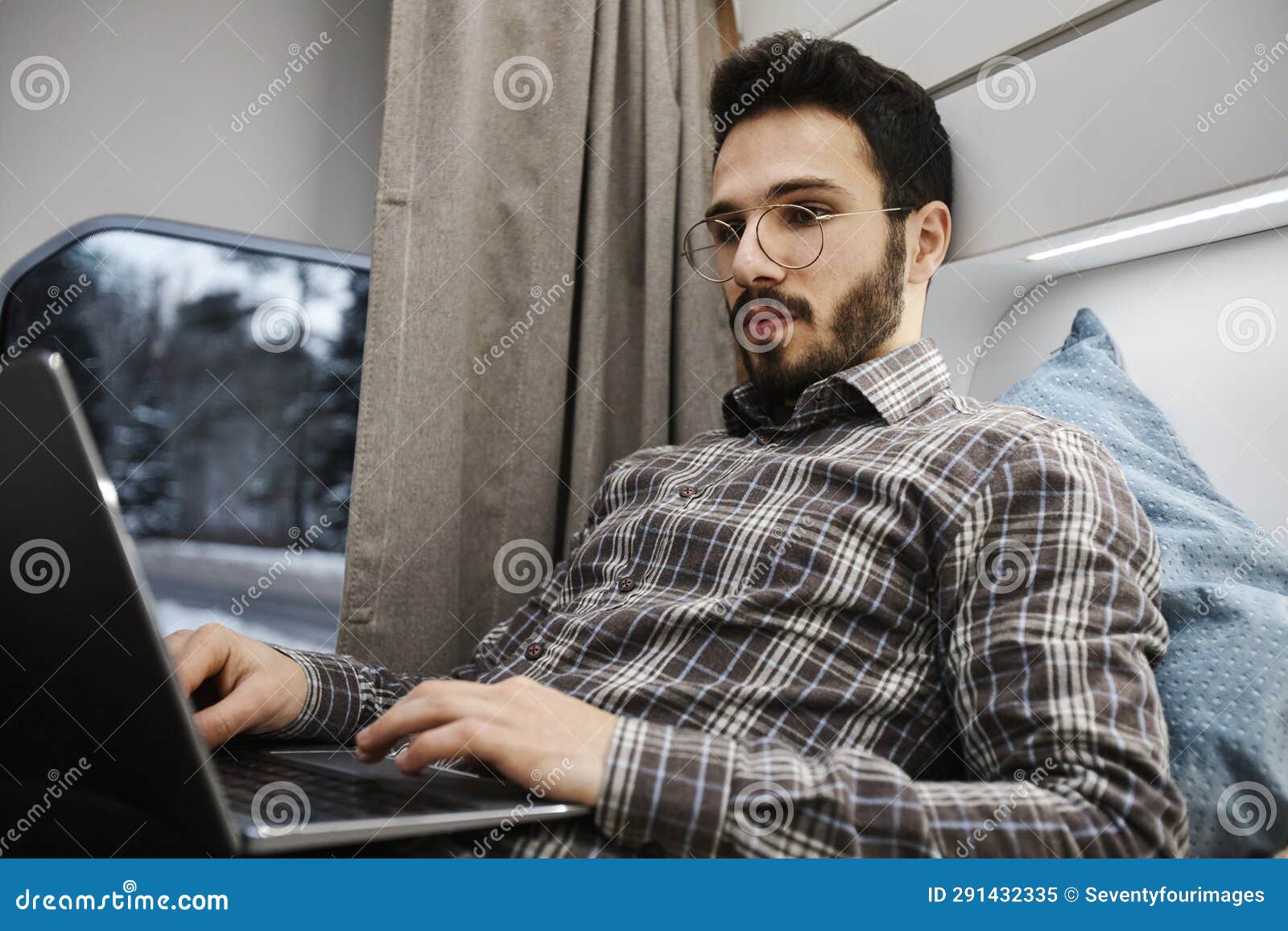 Bearded Young Man Working with Computer in Trailer Van Lying on Bed ...