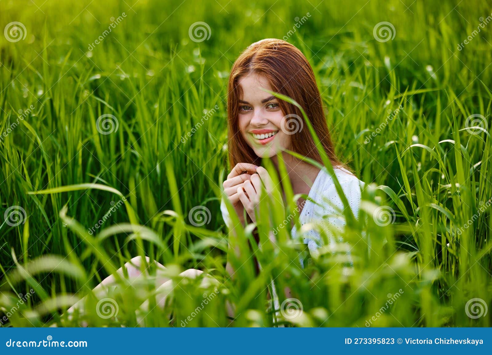 Portrait Of A Beautiful Happy Woman Sitting In The Grass In A Light