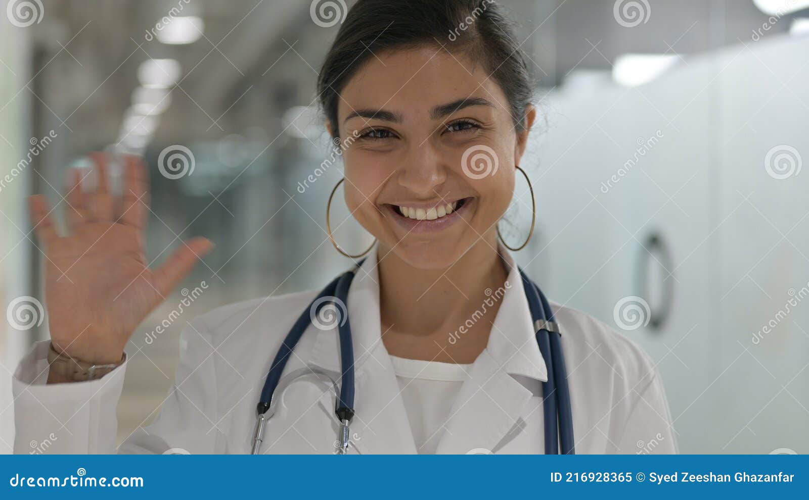 Portrait Of Cheerful Indian Female Doctor Waving At The Camera Stock