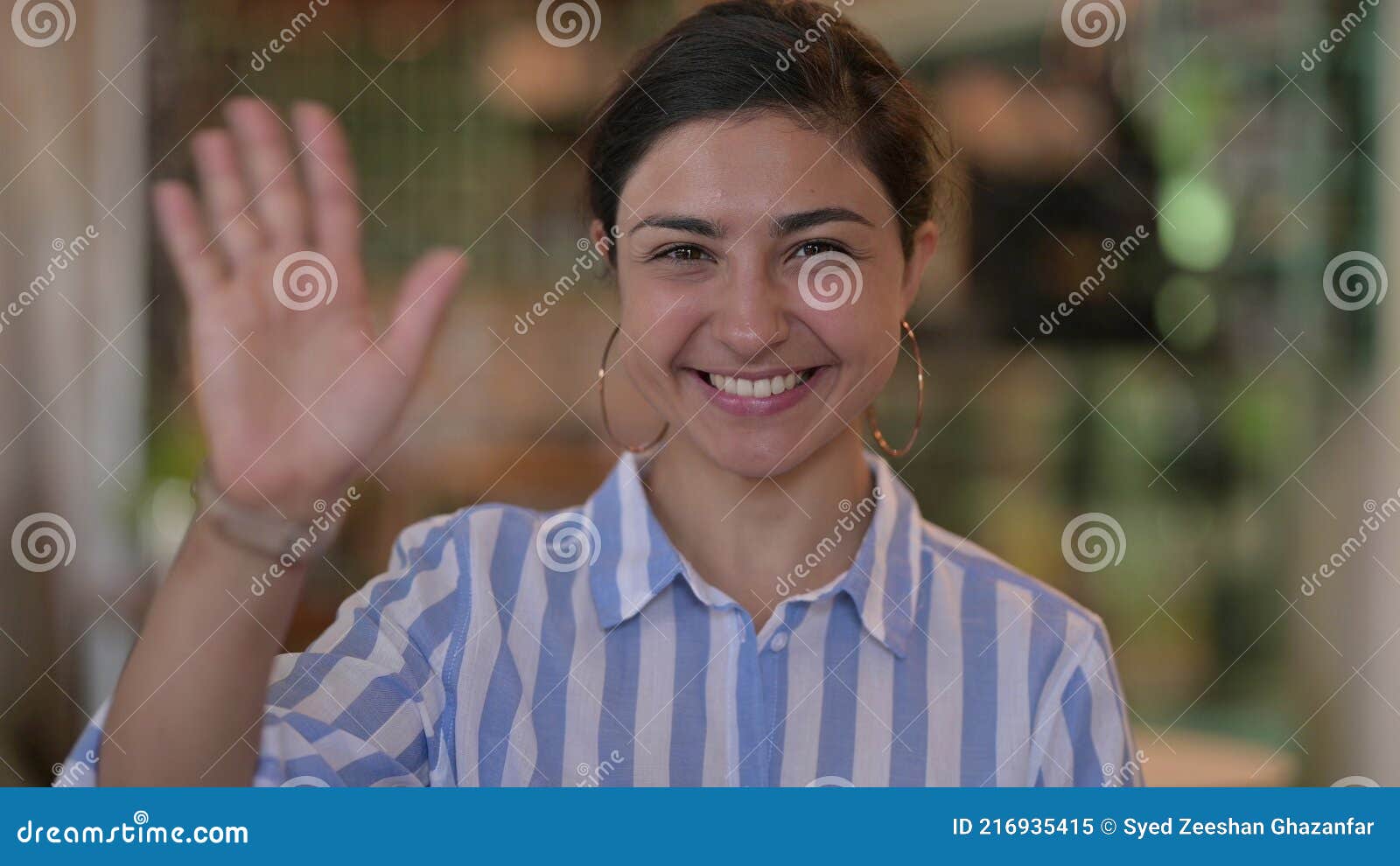 Portrait Of Cheerful Young Indian Woman Waving At The Camera Stock