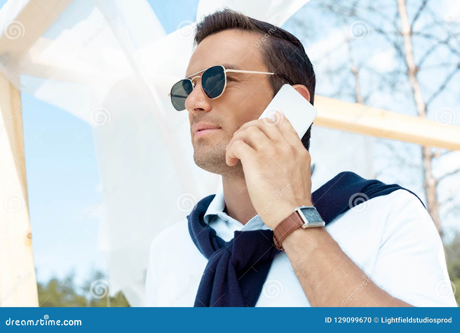 Portrait Of Handsome Man In Sunglasses Talking On Smartphone With Blue
