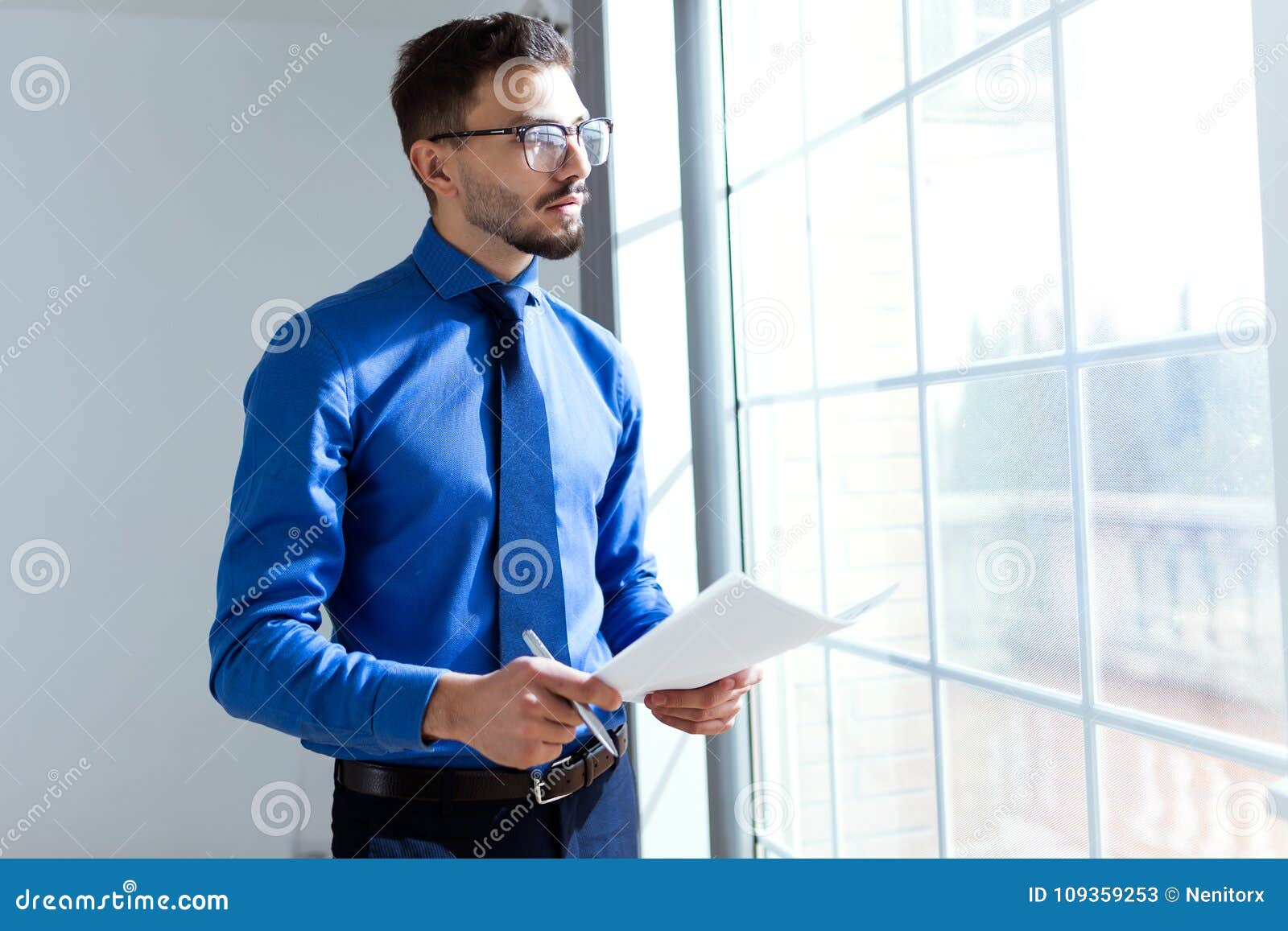 Handsome Young Businessman Holding Papers and Looking Sideways in the ... Handsome Young Businessman Holding Papers and Looking Sideways in the ...