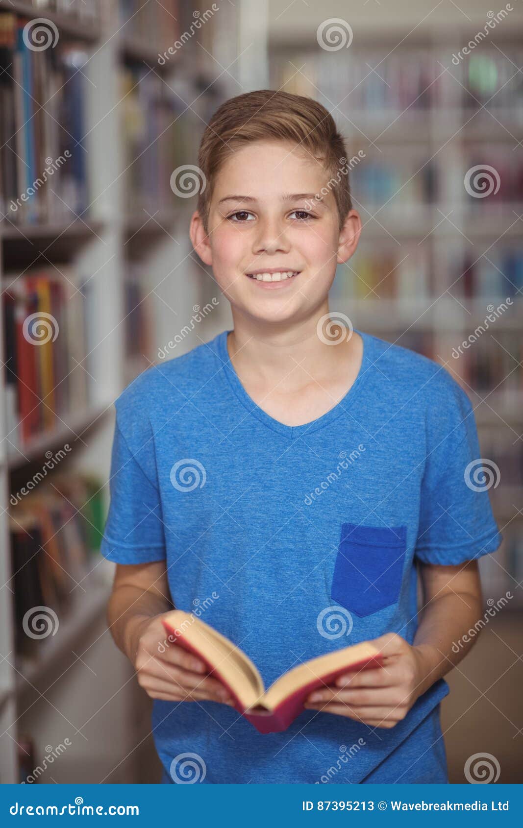 Portrait of Happy Schoolboy Holding Book in Library Stock Image - Image ...
