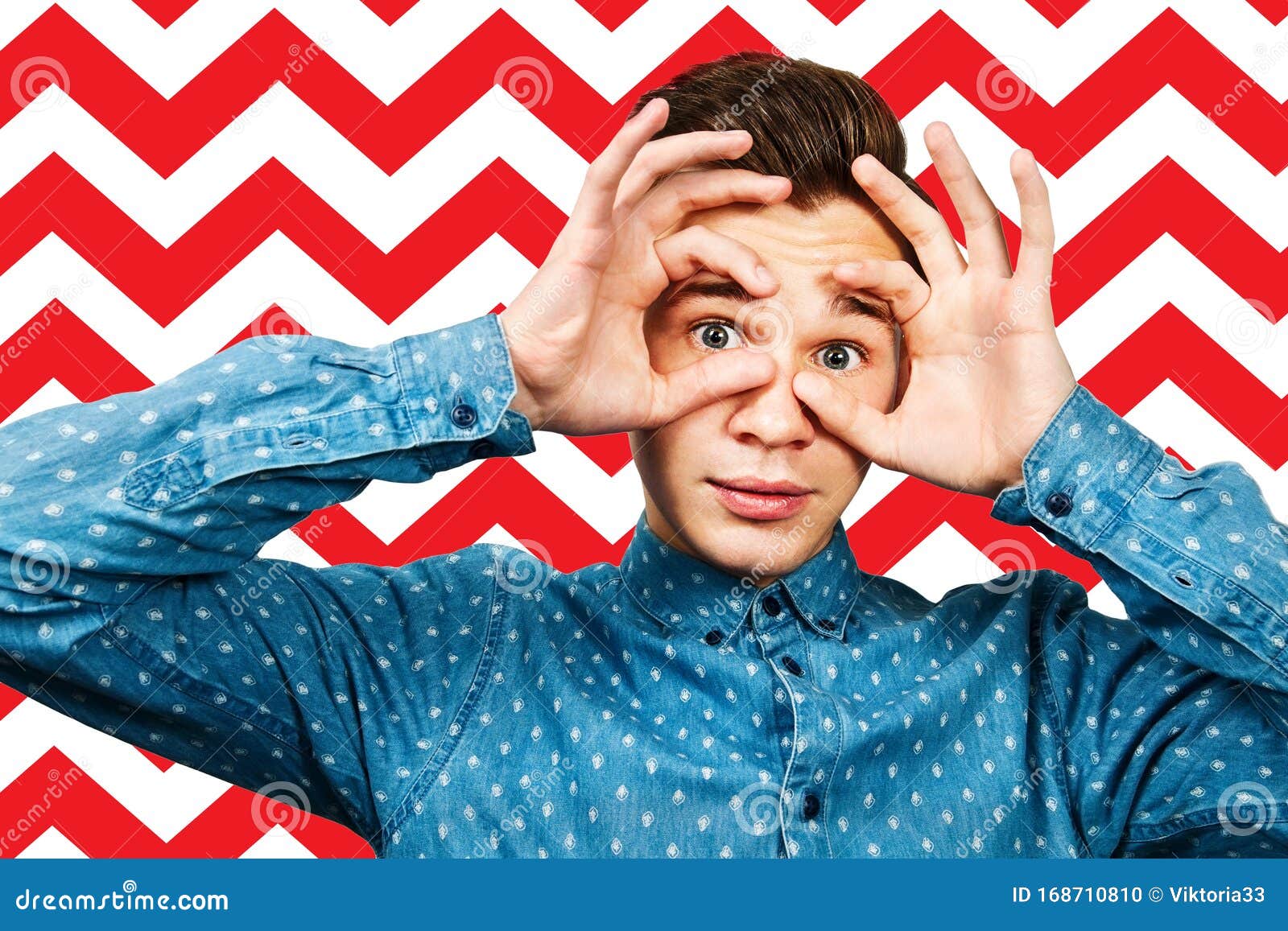 Portrait Of Joyful Guy 30s Having Fun And Looking On Camera Through Holes Like Binoculars On Red