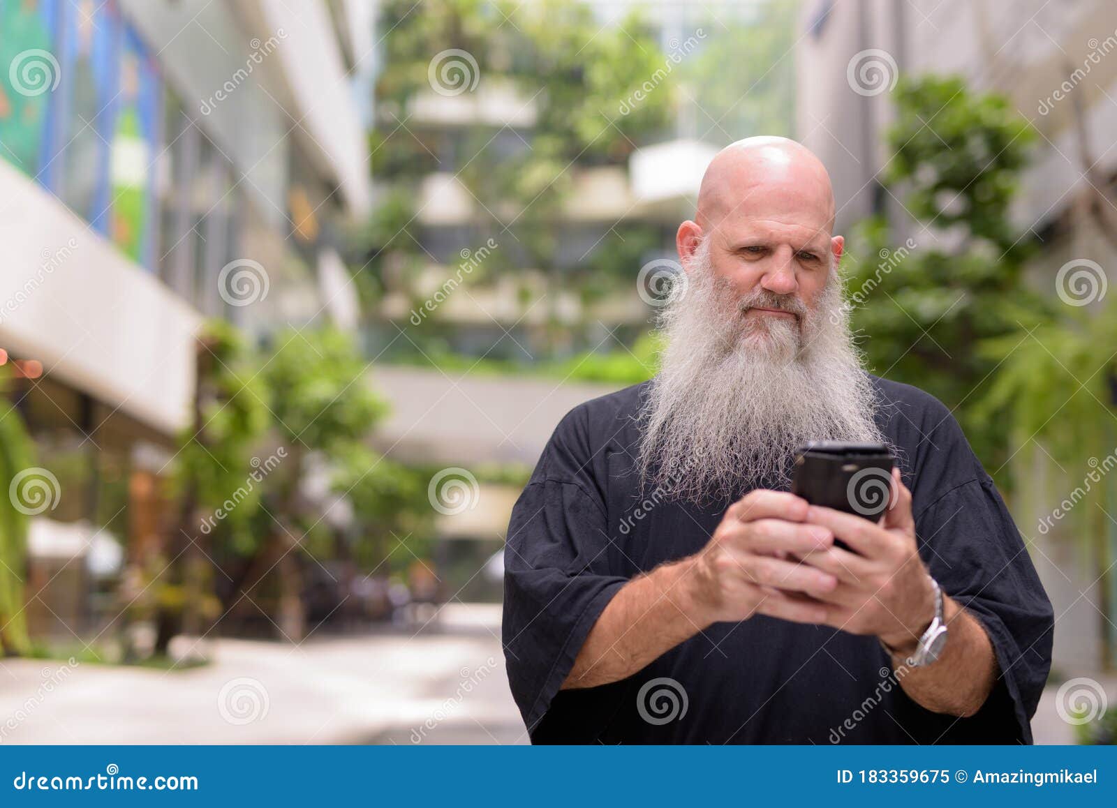 Mature Handsome Bald Bearded Man Using Phone With Nature In The City