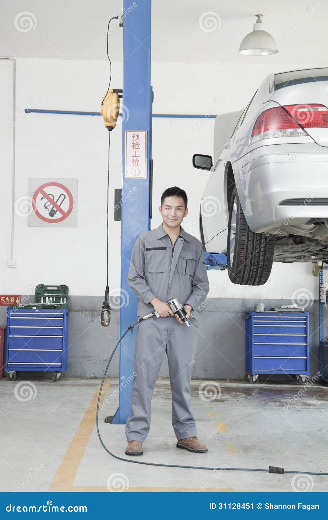 Portrait of Mechanic with Power Tool Next To Car Wheel, Looking at ...