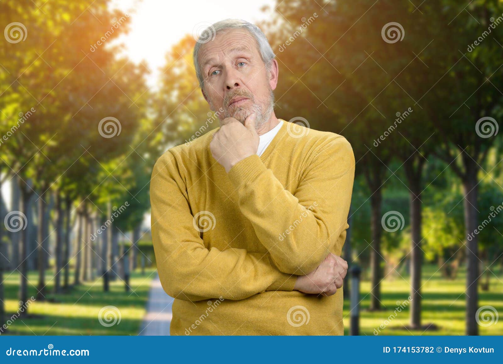 Portrait Of Old Thoughtful Man In Park With Green Background Stock