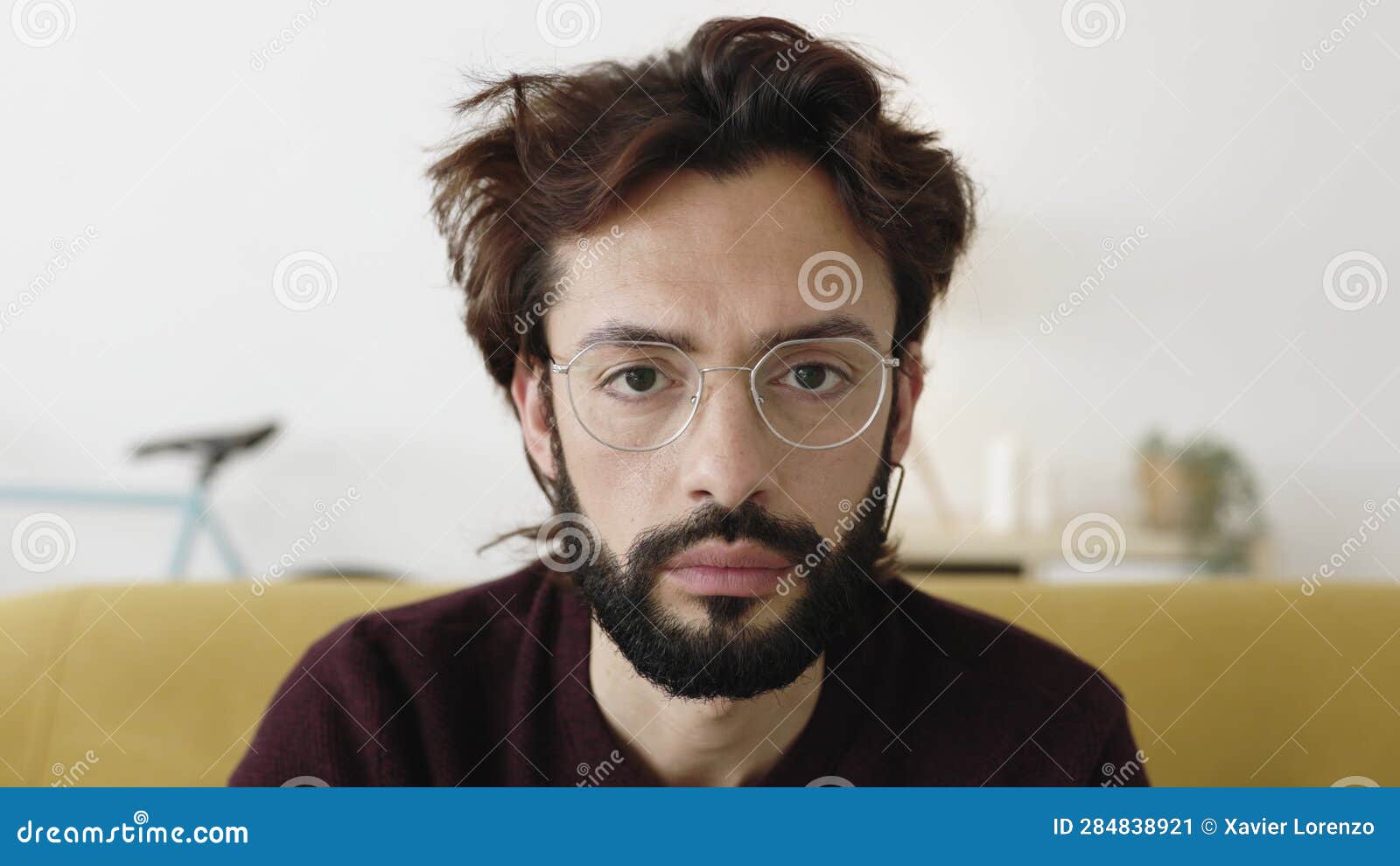 Portrait Of Serious Bearded Man Looking At Camera Sitting On Couch At