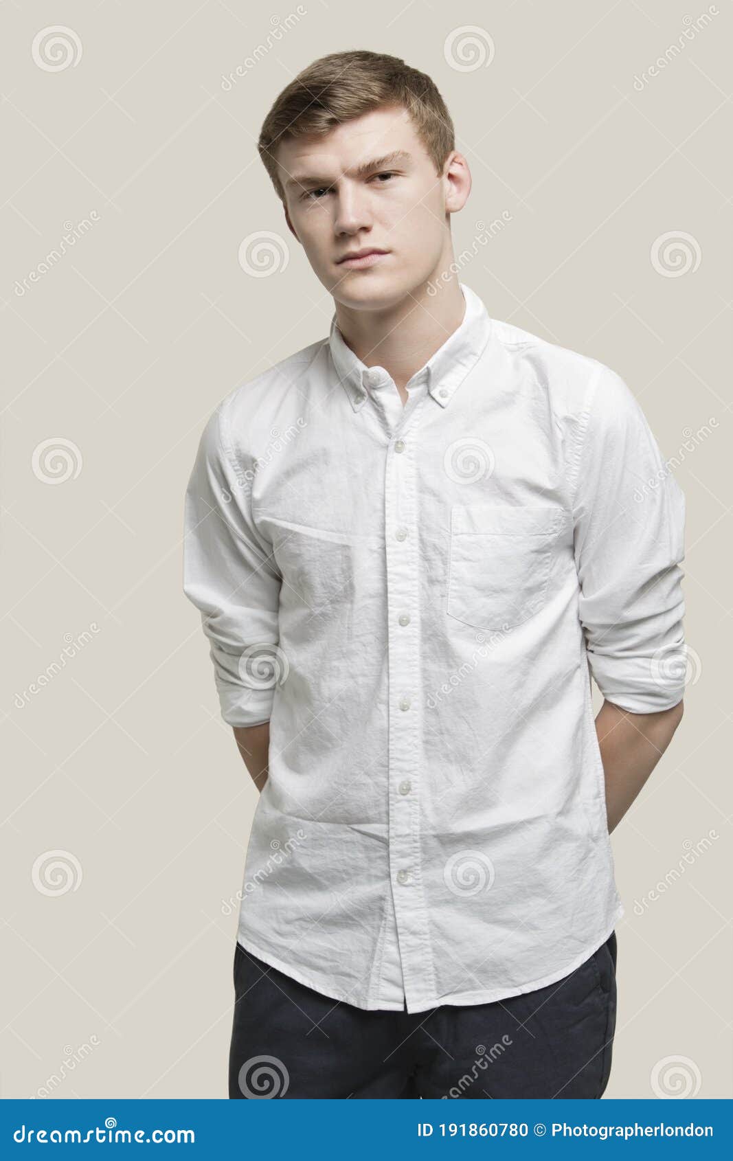 Portrait Of Serious Young Man With Hands Behind Back Against Gray ... Portrait Of Serious Young Man With Hands Behind Back Against Gray ...