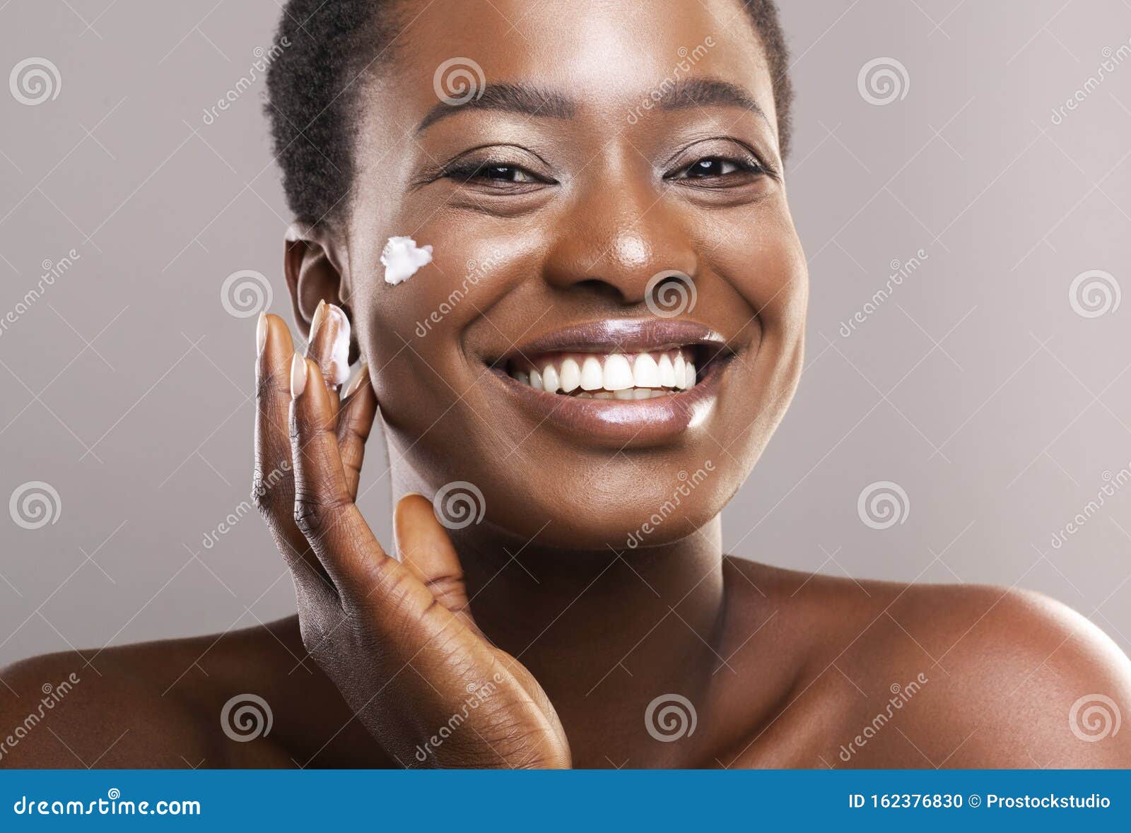 Portrait Of Smiling Black Woman Applying Moisturizing Cream On Face