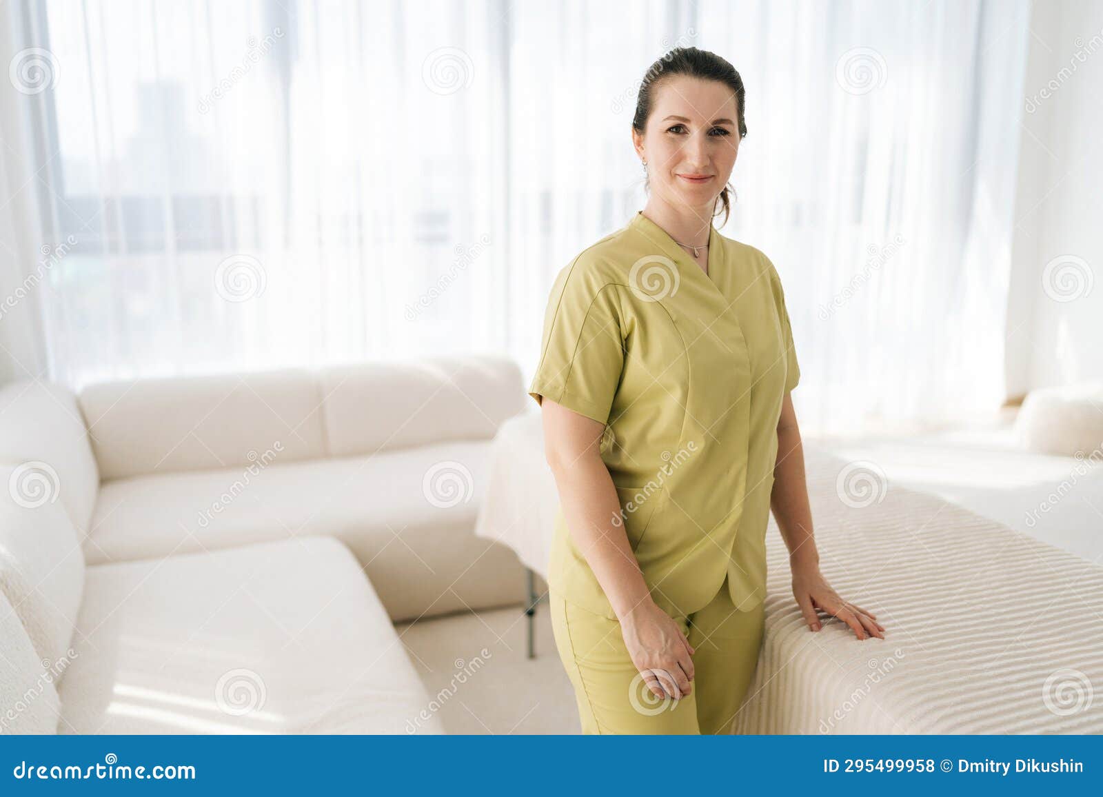 Portrait Of Smiling Female Masseuse Therapist In Uniform Standing Posing By Working Couch