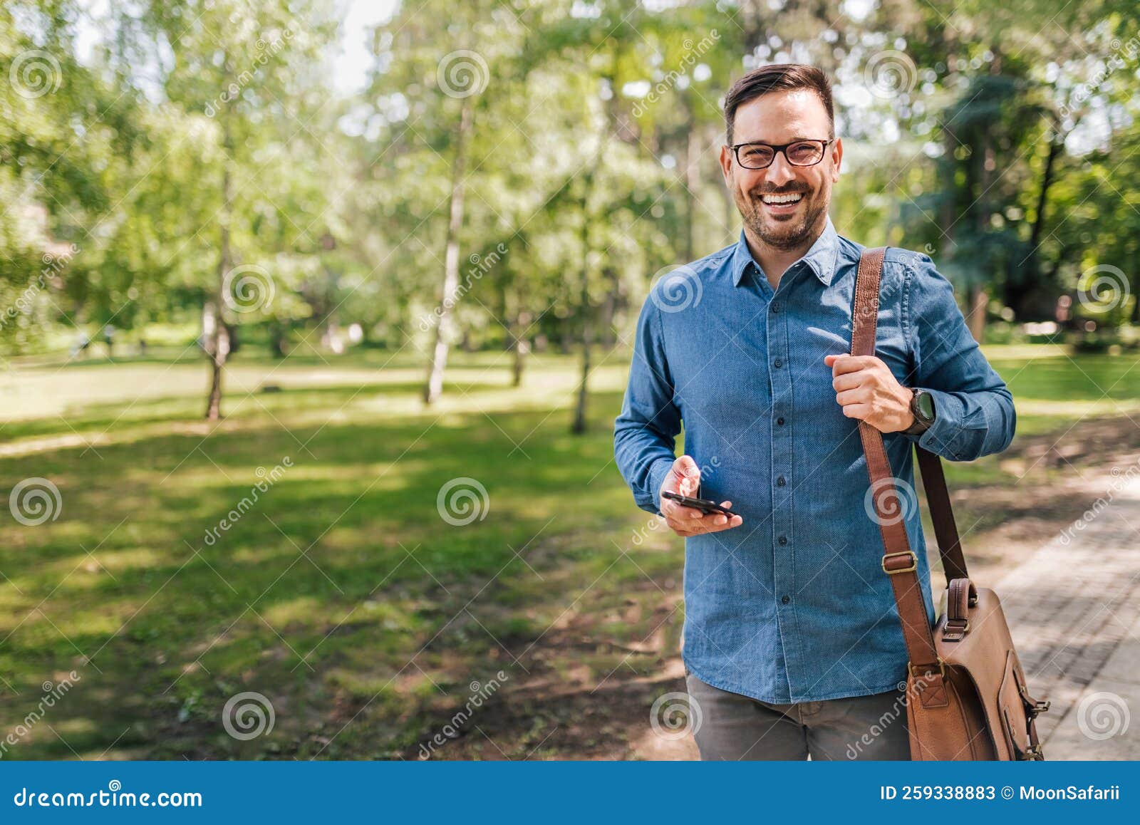 Portrait of Smiling Young Adult Man, Walking through the Park, Using ... Portrait of Smiling Young Adult Man, Walking through the Park, Using ...