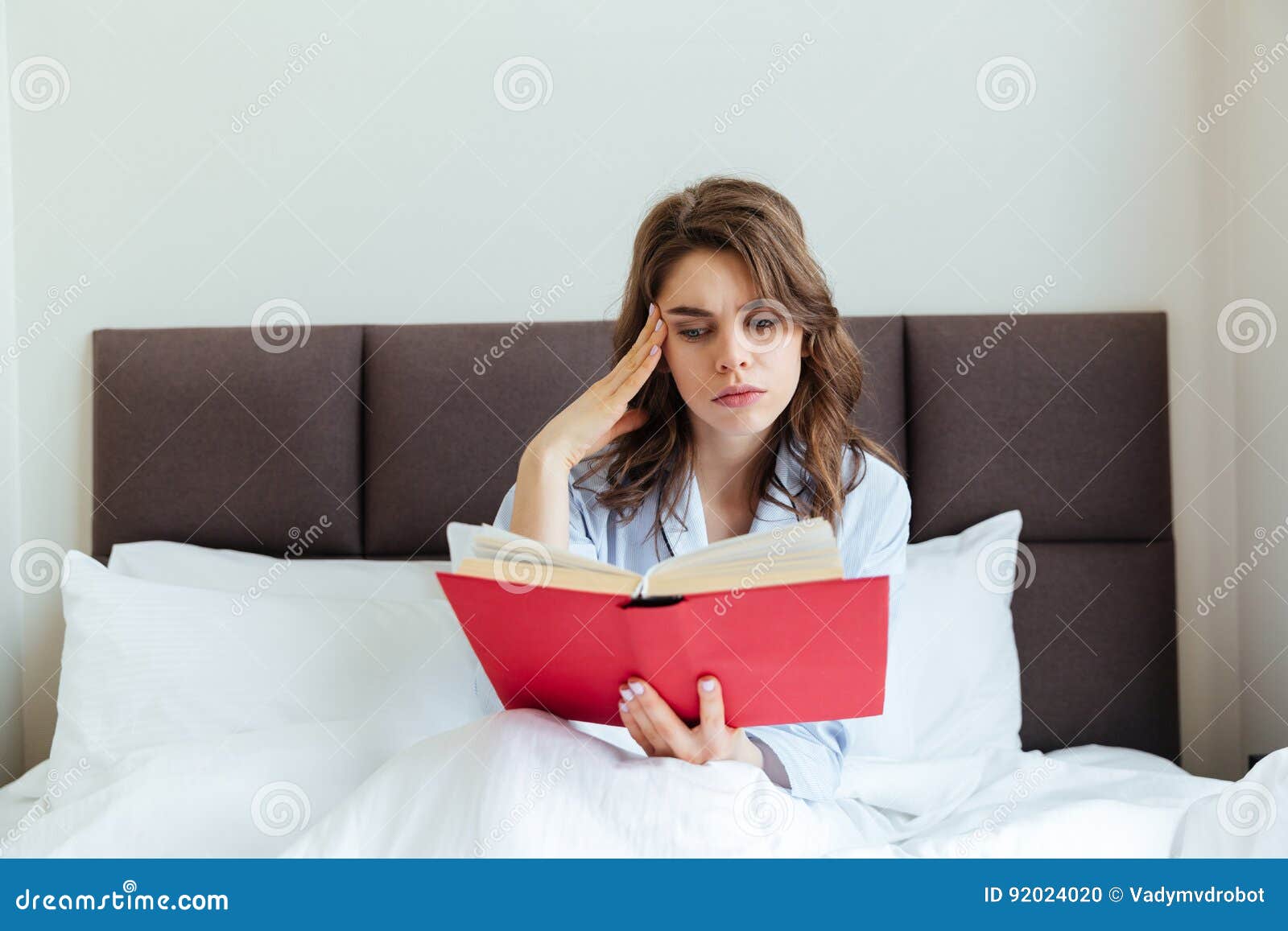 Portrait Of A Thoughtful Young Woman In Pajamas Reading Book Stock