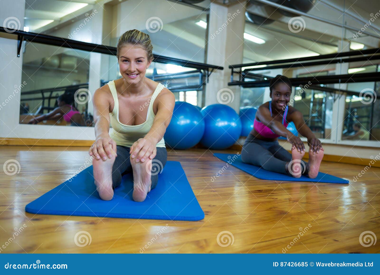 Portrait Of Two Smiling Women Doing Stretching Exercise On Mat Stock