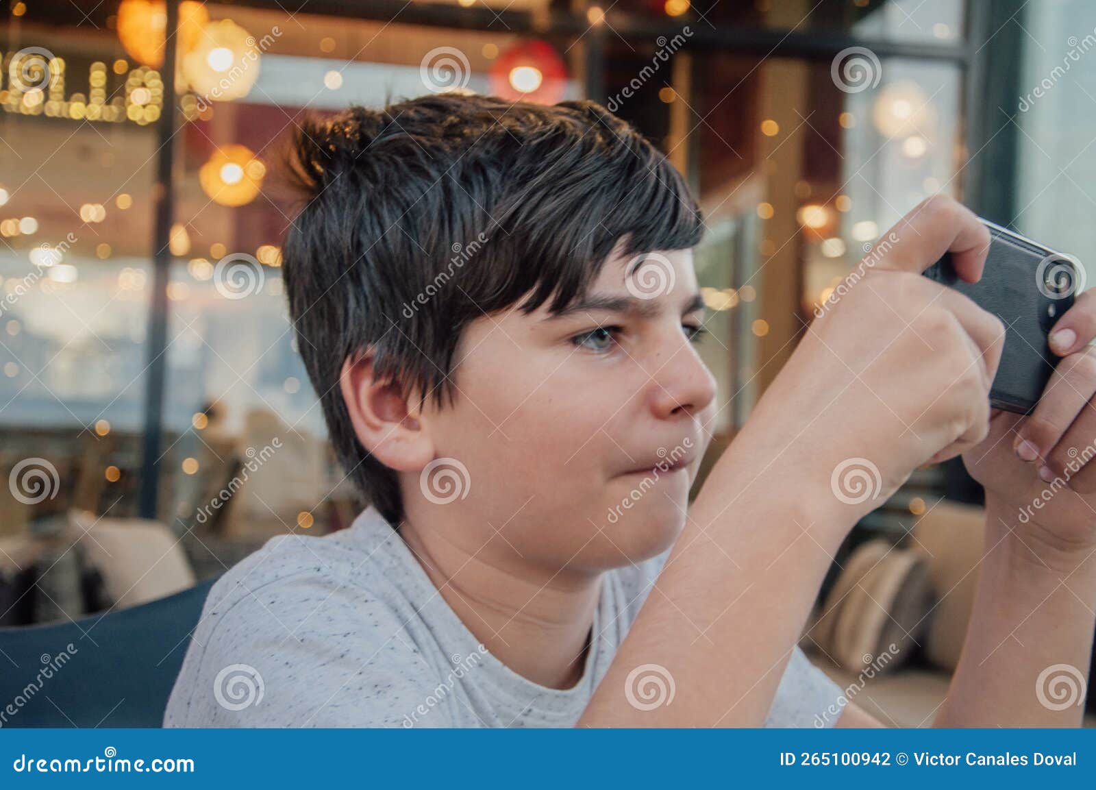 Portrait of Young Boy Playing Mobile Phone Games in a Bar, with ...