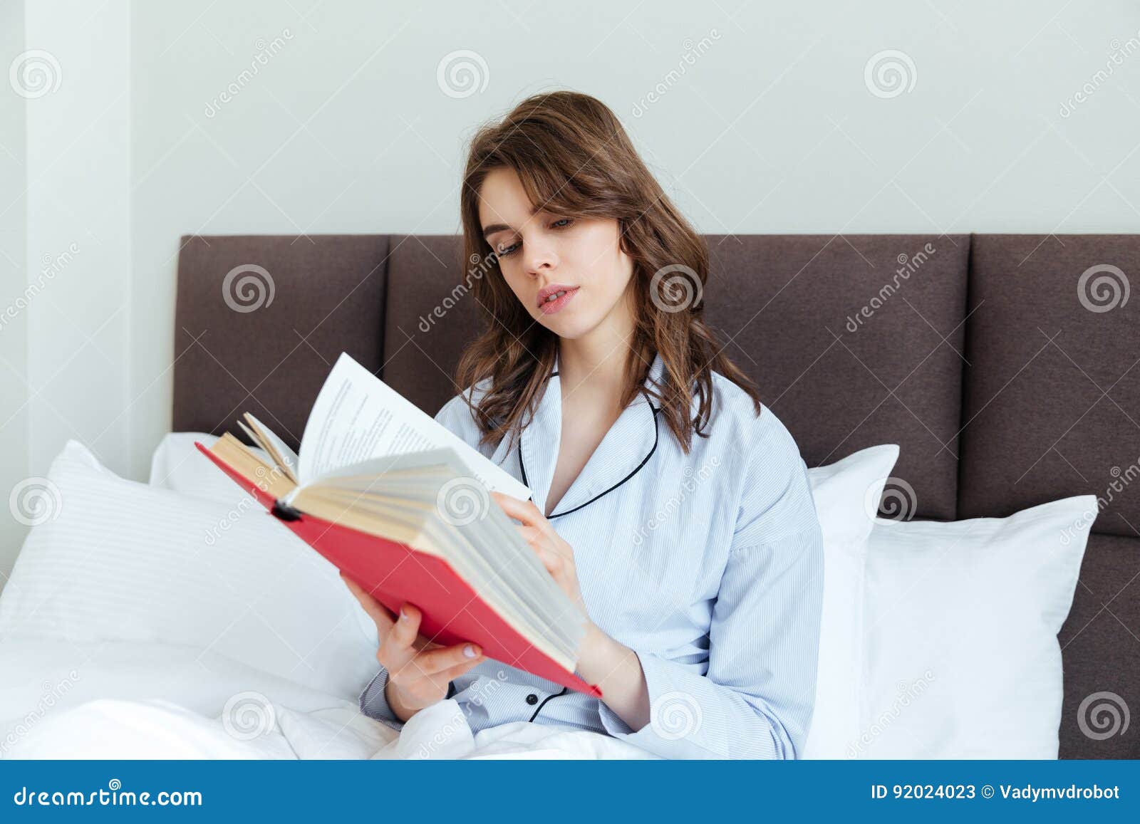 Portrait Of A Young Brunette Woman In Pajamas Reading Book Stock Image