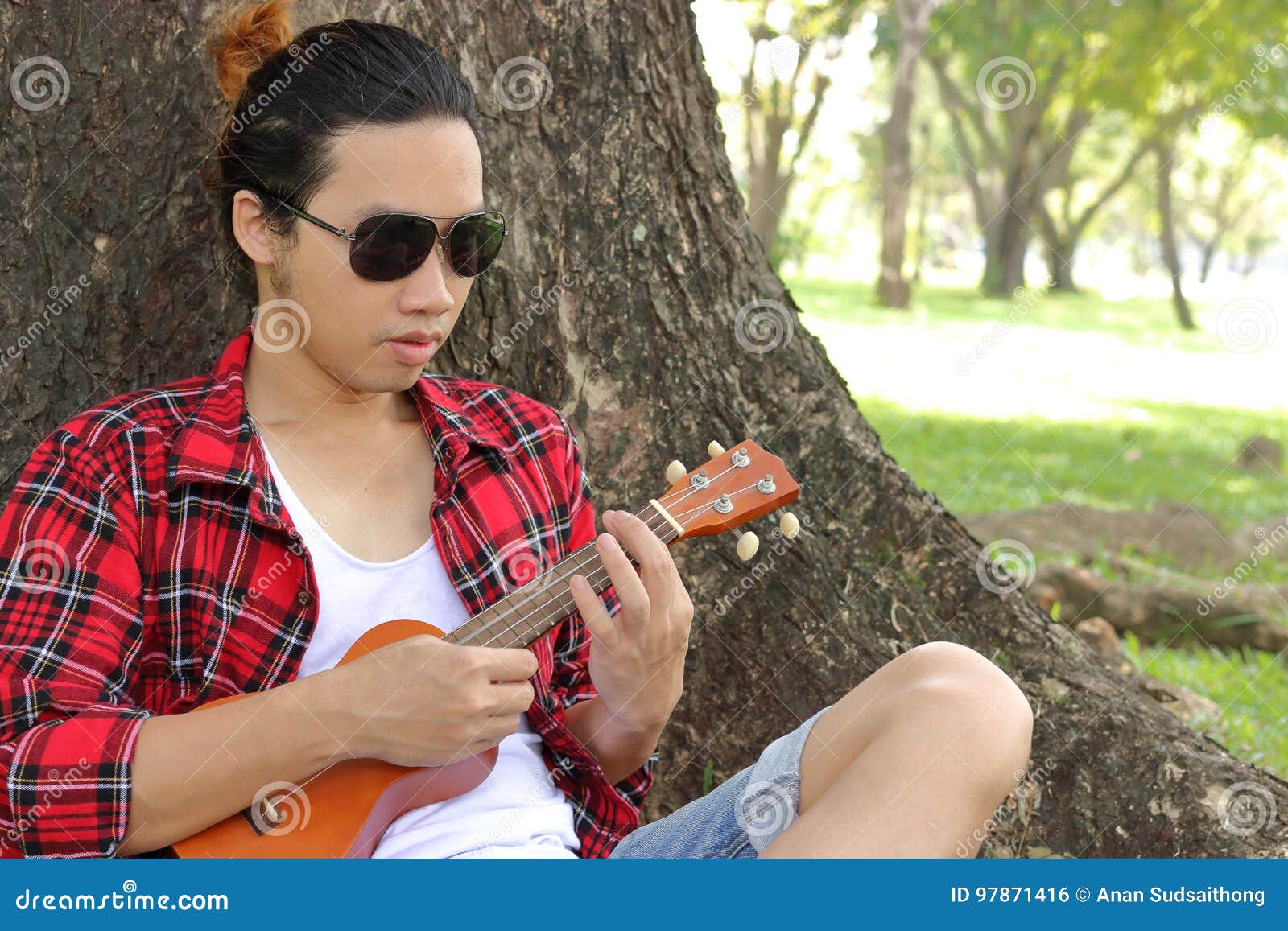 Portrait Of Young Man Playing Ukulele In Public Outdoor Park Stock