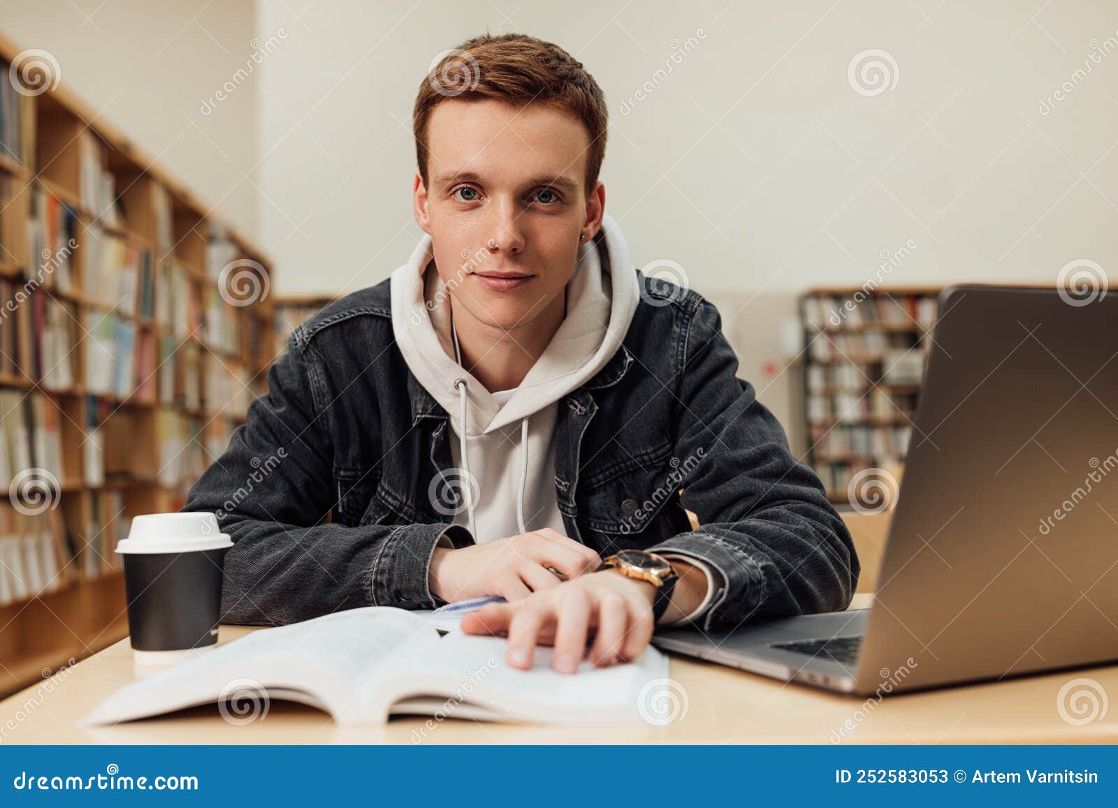Portrait of a Young Man Sitting at Desk in Library and Looking at ...