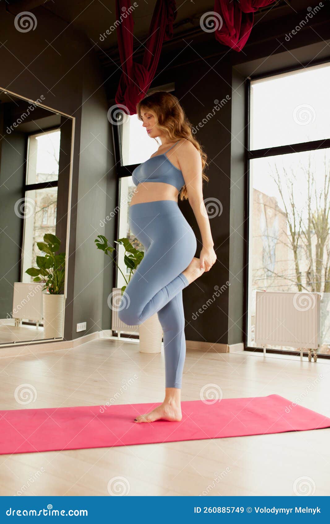 Portrait Of Young Pregnant Woman Standing On Mat And Stretching Legs