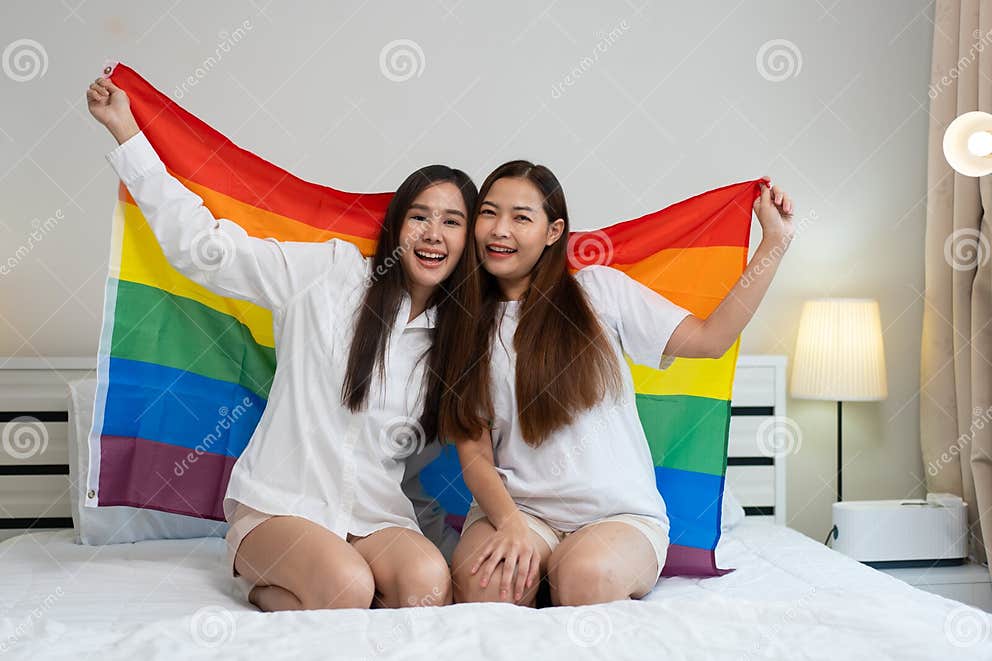 Portraits Of Happy Asian Lesbian Couple Sitting With Rainbow Flag