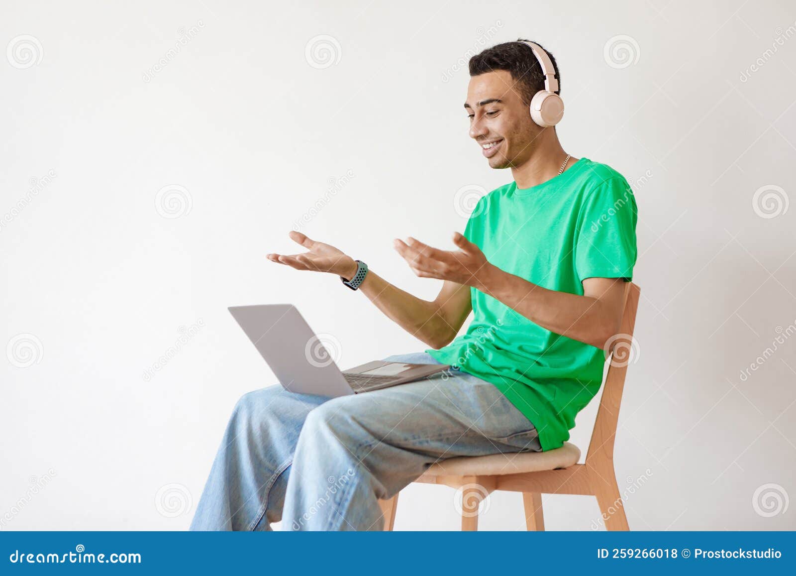 Positive Arab Guy Sitting on Chair Over Light Wall, Using Laptop and ...