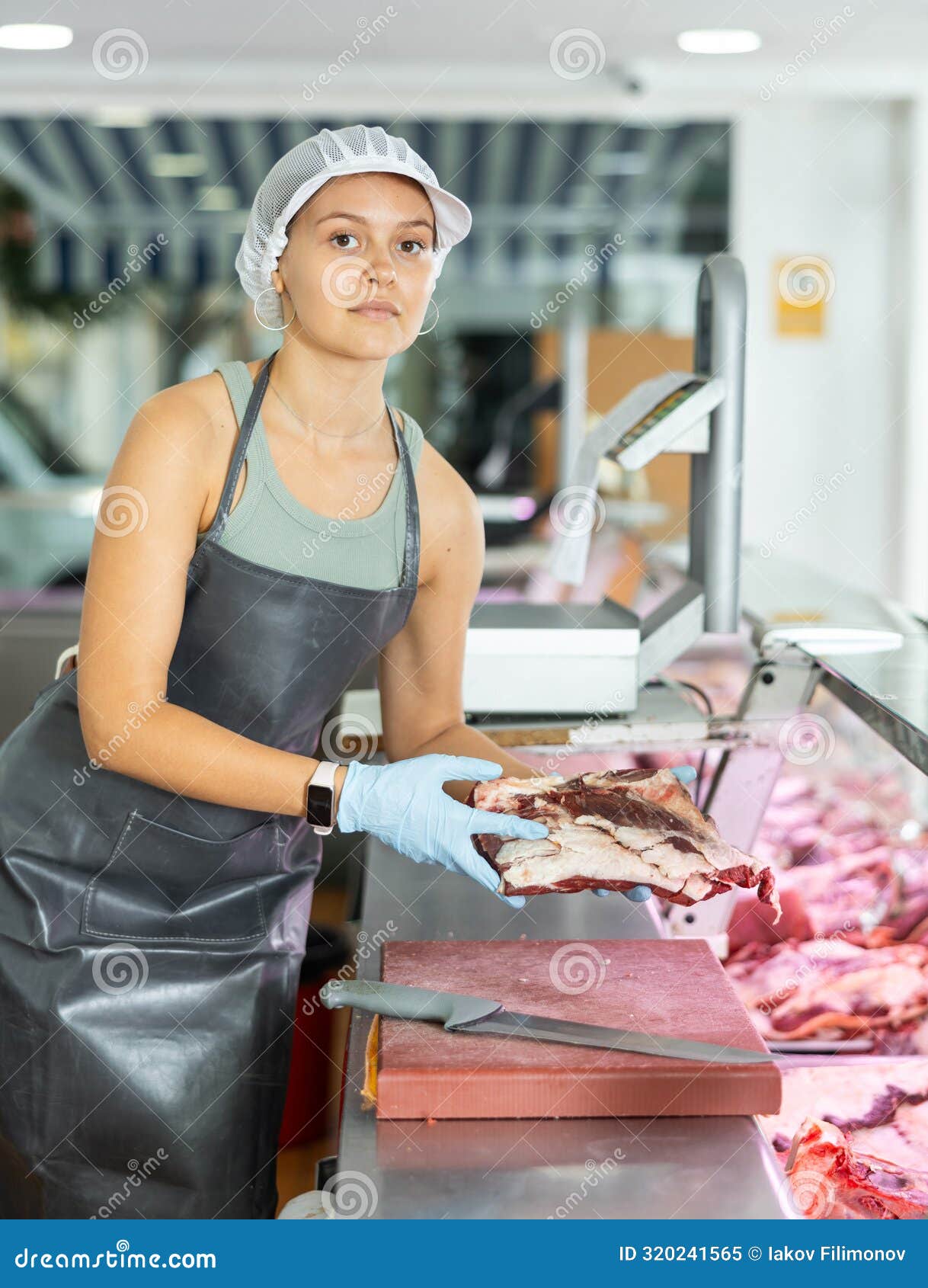 Positive Young Saleswoman Demonstrating Piece Of Meat In Butcher Shop