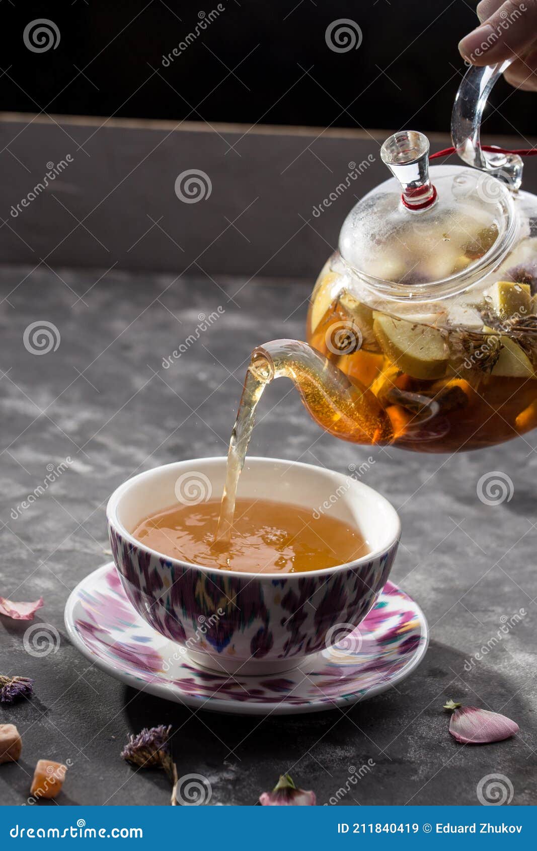 Pouring Tea from Transparent Teapot with Fresh Apple and Flowers on the ...