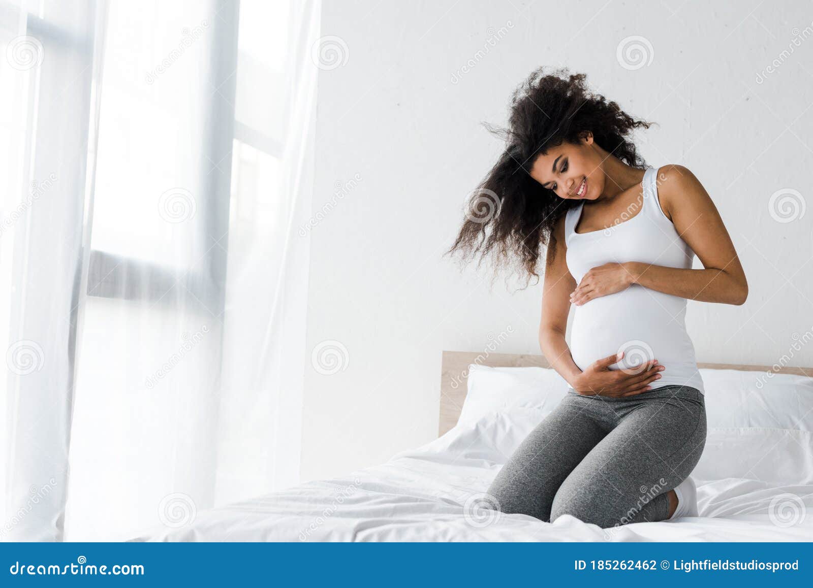Pregnant African American Woman Touching Belly While Sitting On Bed