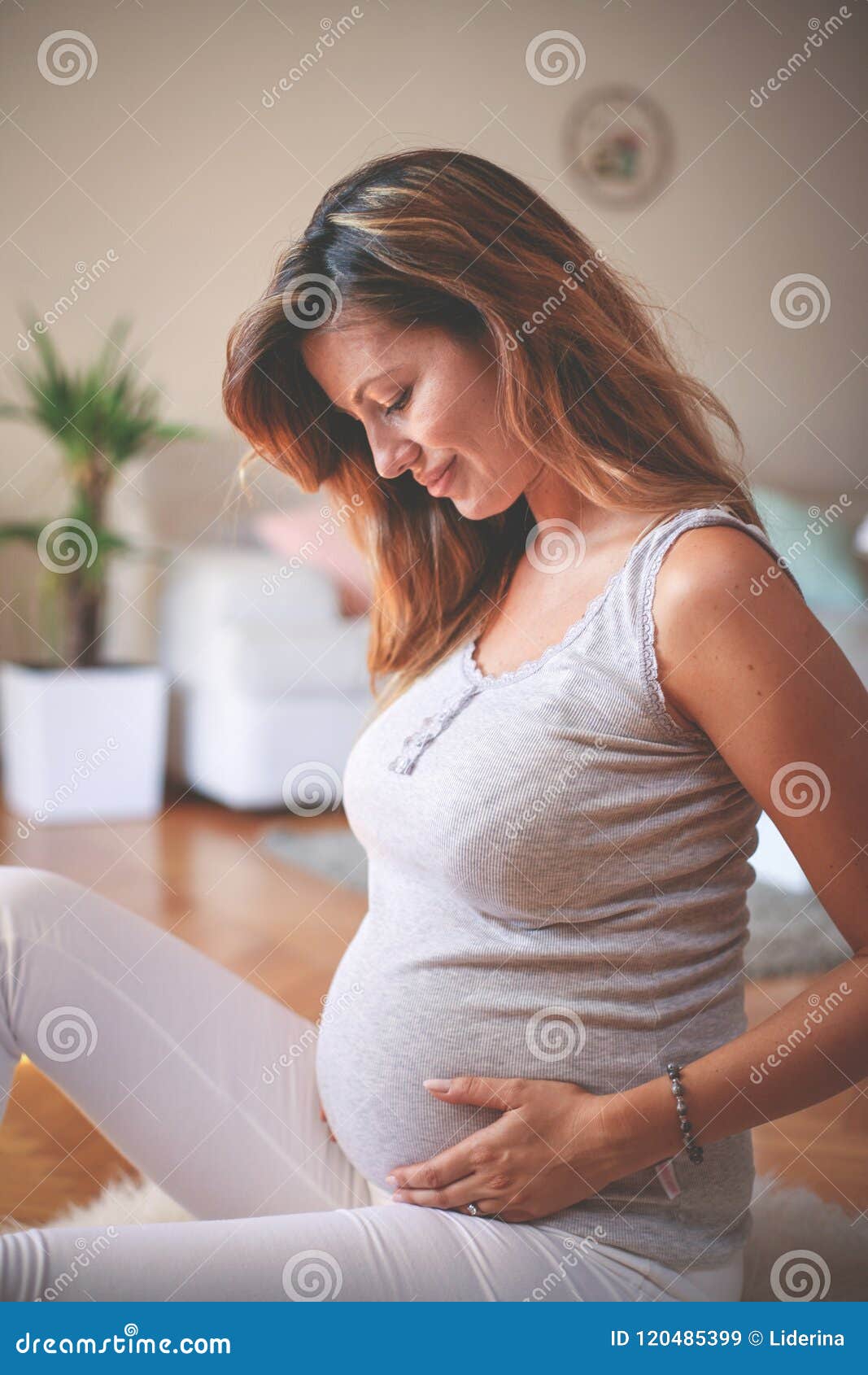 Pregnant Brunette Woman Touching Her Belly And Sitting On Floor Stock