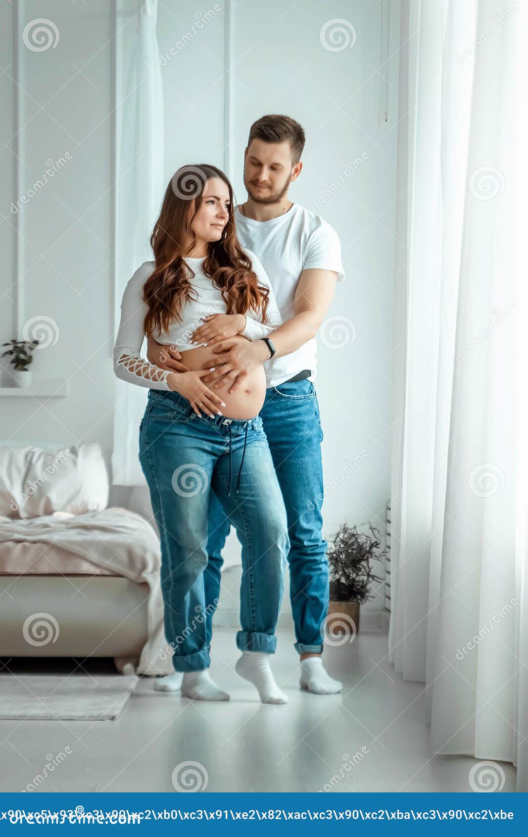 A Pregnant Girl With Her Husband Are Standing In A Bright Bedroom