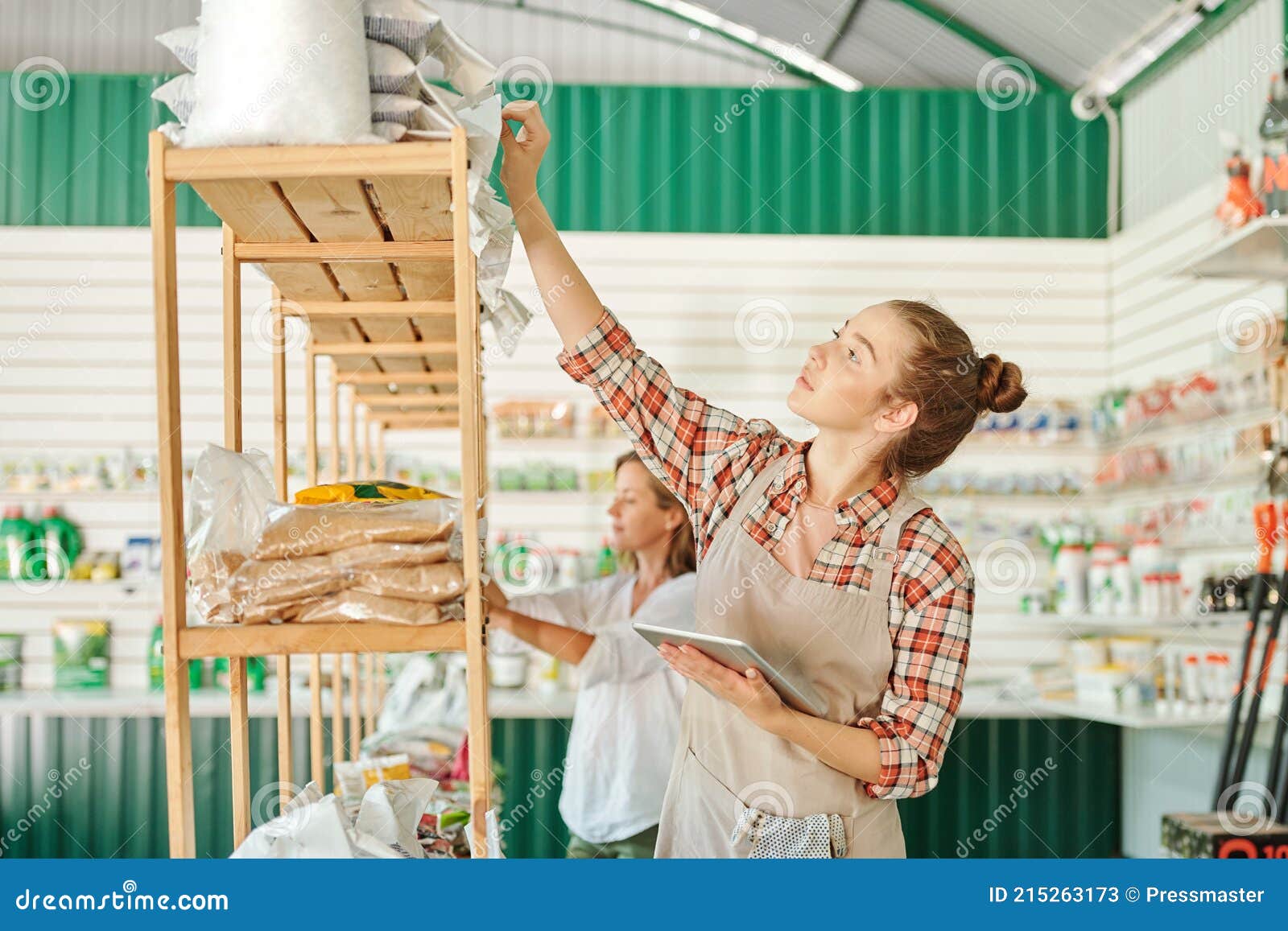 Pretty Assistant in Workwear Standing by Shelf with Packed Fertilizers ...