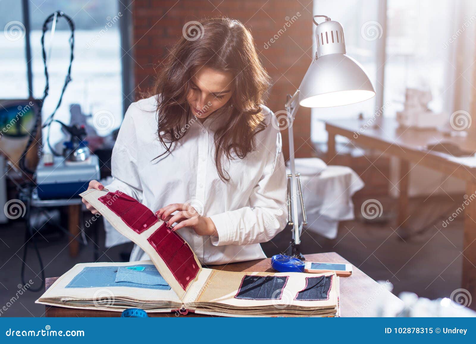 Pretty Female Tailor Choosing a Fabric in Cloths Catalog in Studio ...