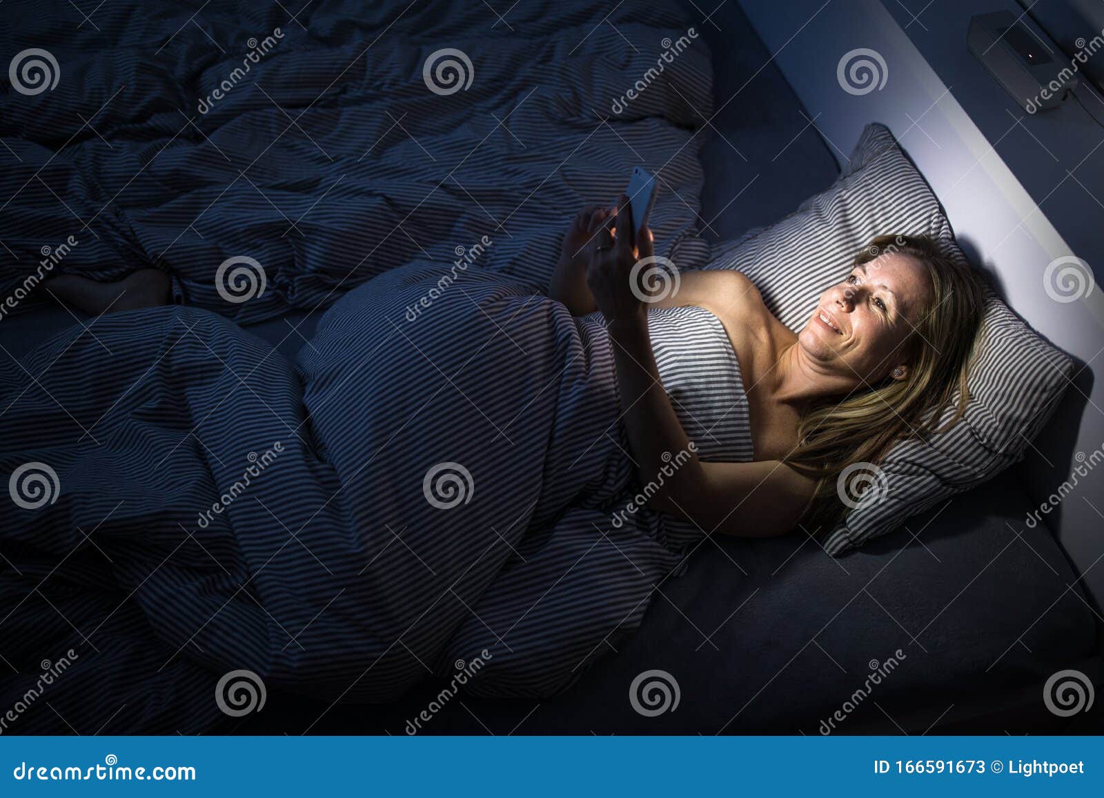 Pretty Middle Aged Woman Using Her Cell Phone In Bed Stock Image