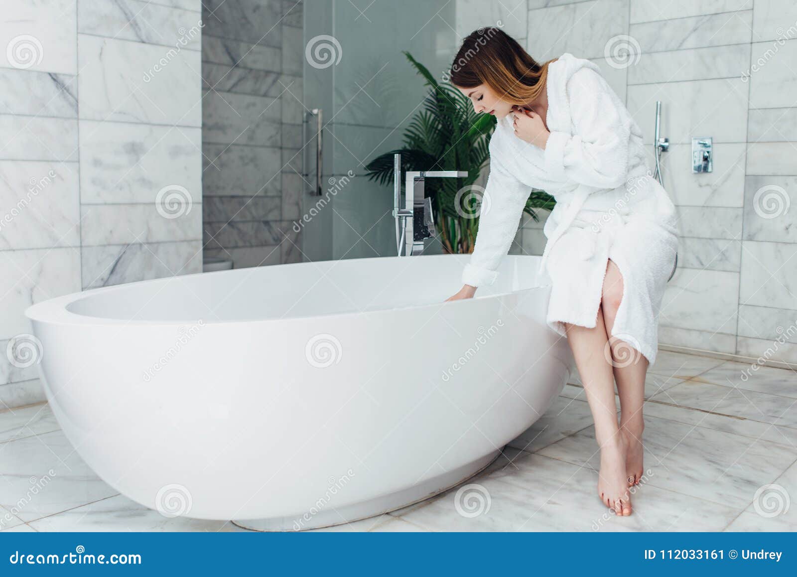 Pretty Slim Woman Wearing Bathrobe Sitting on Edge of Bathtub Filling ... Pretty Slim Woman Wearing Bathrobe Sitting on Edge of Bathtub Filling ...