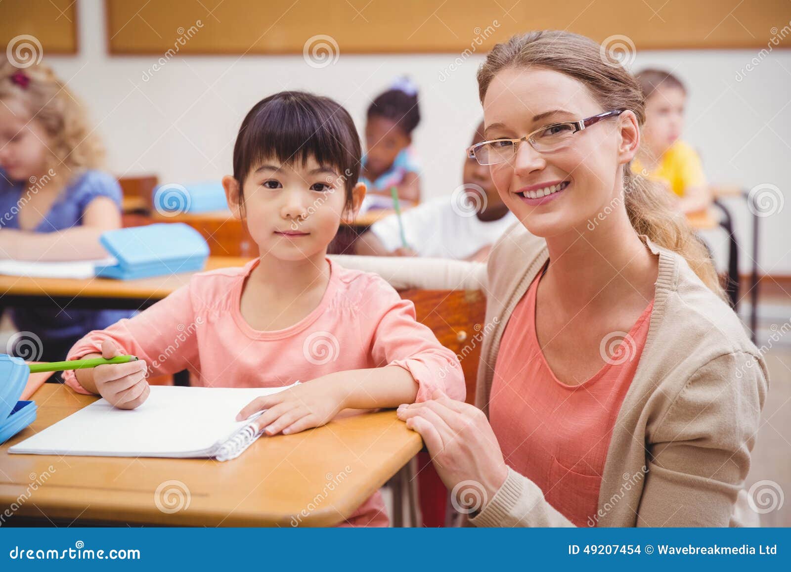 Pretty Teacher Helping Pupil in Classroom Smiling at Camera Stock Photo ...
