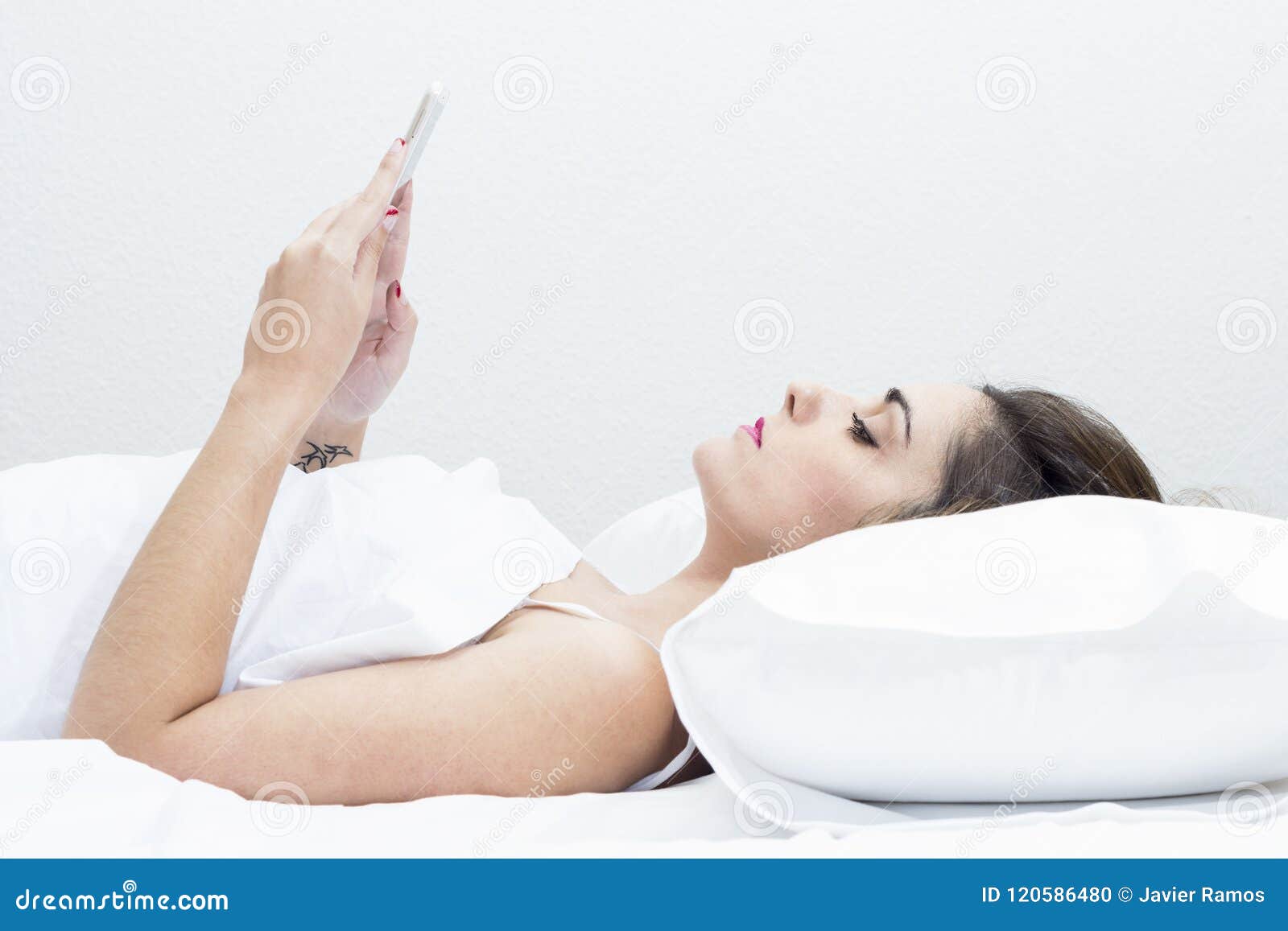 Pretty Woman Lying on a White Bed Face Up with Mobile Hands Stock Photo ...