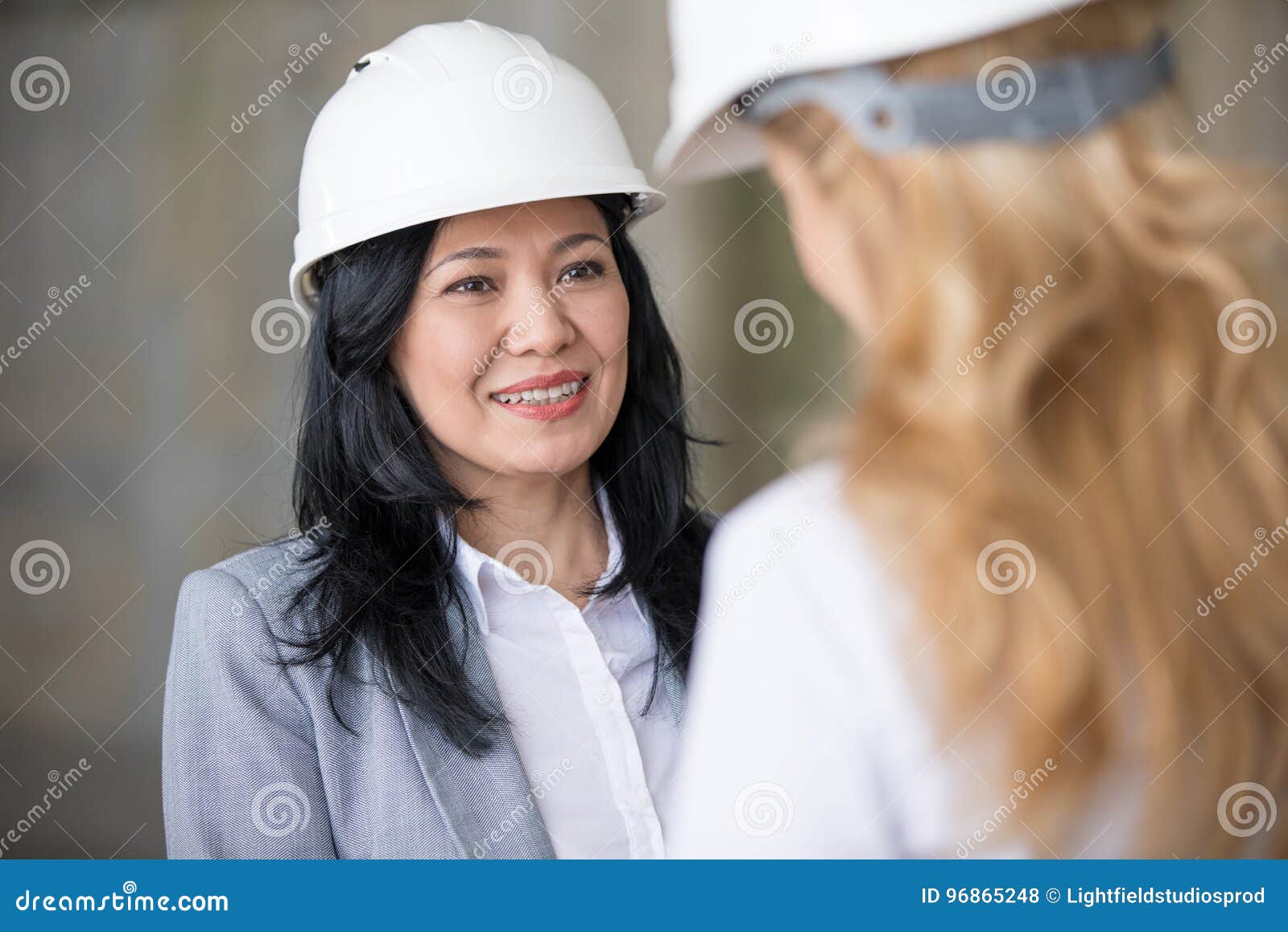 Professional Architect in Hard Hat Looking at Blonde Colleague while ... Professional Architect in Hard Hat Looking at Blonde Colleague while ...
