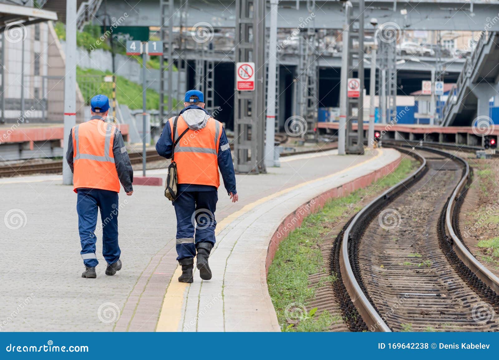 Railway Workers on Passenger Platform. Technological Buildings in the ...