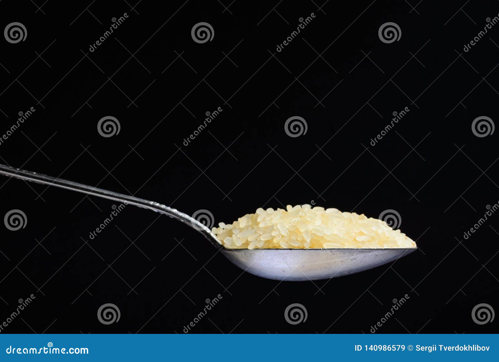Raw Rice Poured into a Silver Spoon. Side View on a Black Background ...