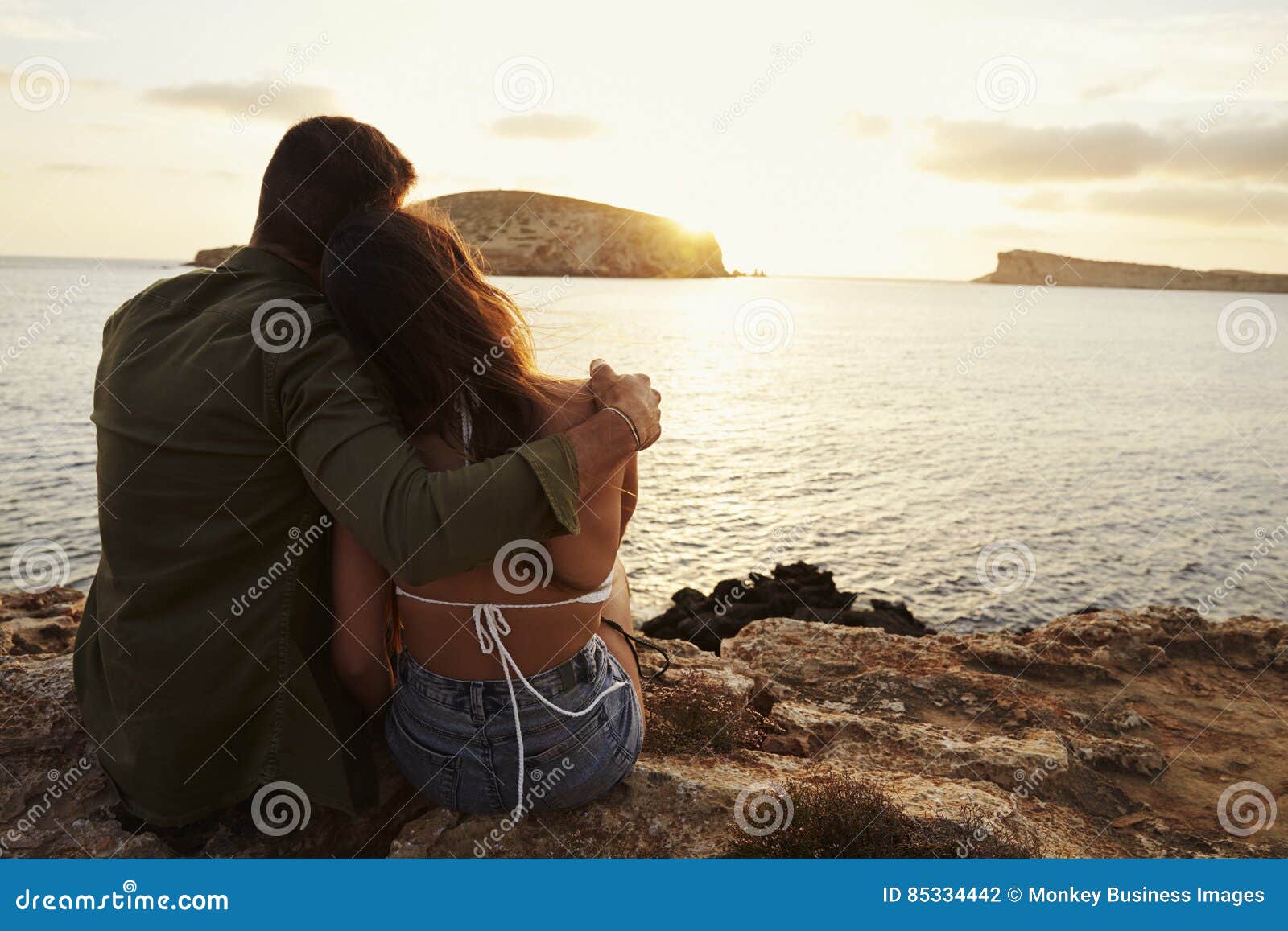 Rear View of Couple Sitting on Cliff Watching Sunset Stock Photo ...