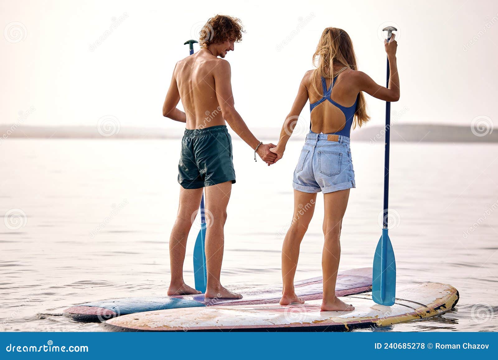 Rear View On Couple Of Surfers Standing On Surfboards Preparing To Surf