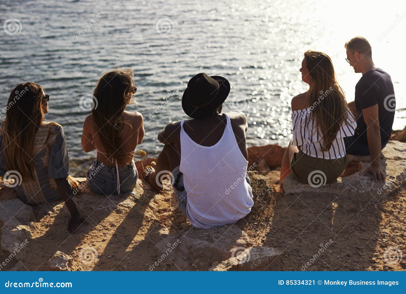Rear View of Friends Sitting on Cliff Watching Sunset Stock Image ...