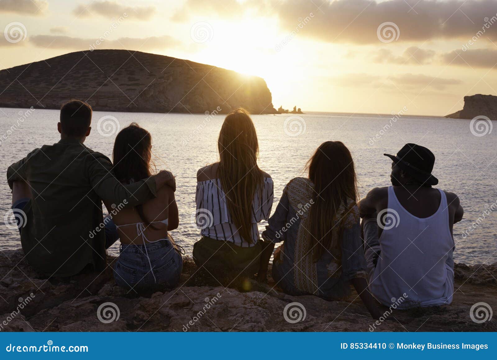 Rear View of Friends Sitting on Cliff Watching Sunset Stock Photo ...