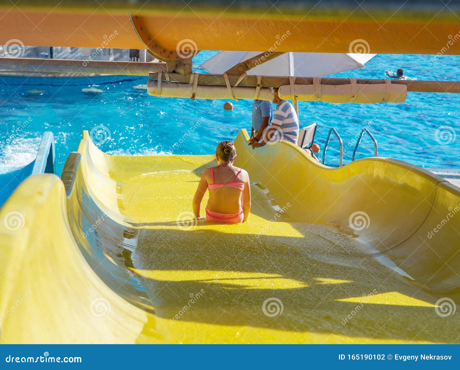 Rear View Of A Girl Sliding Down A Water Slide Into A Swimming Pool On