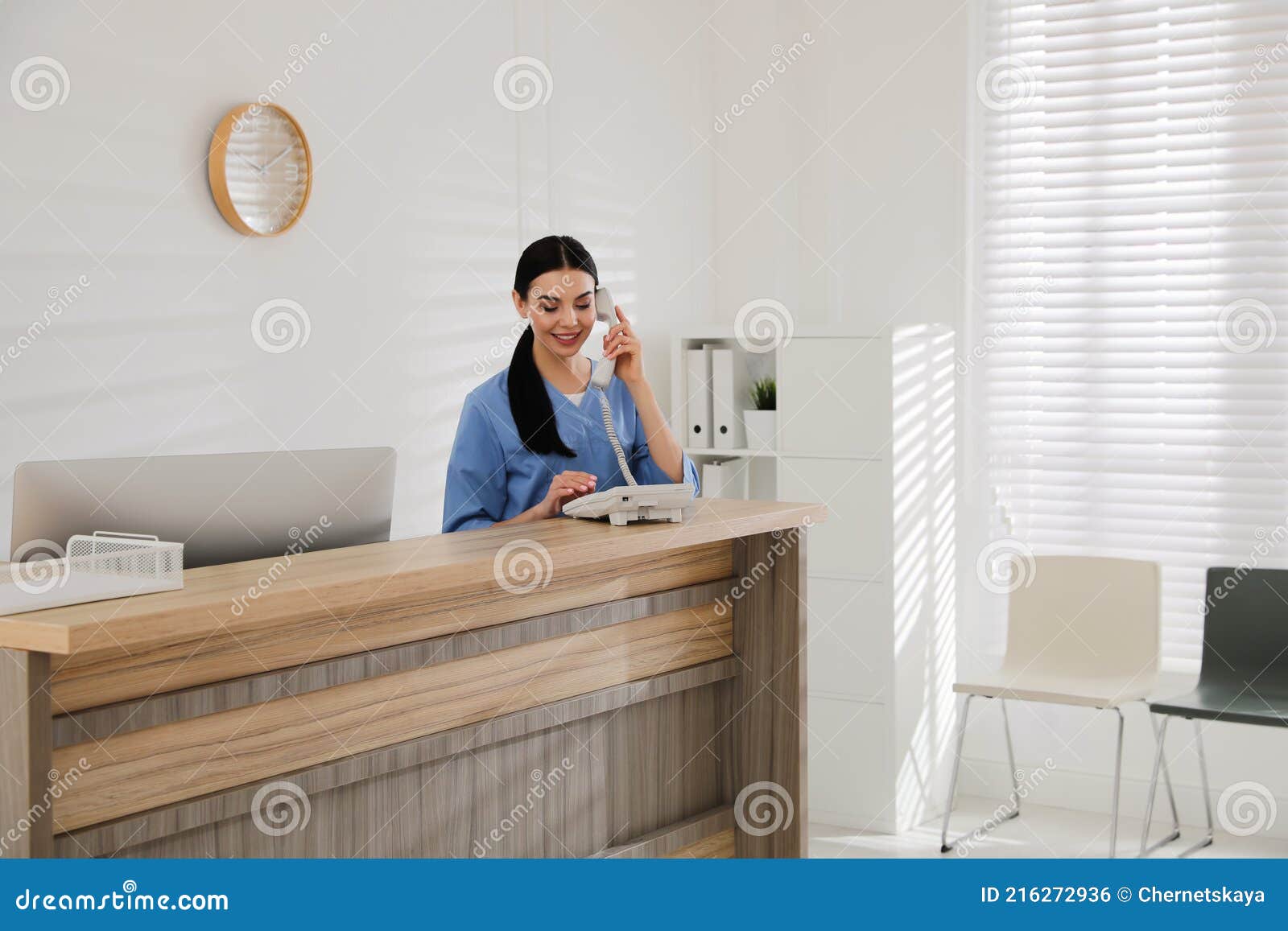 Receptionist Talking on Phone at Countertop in Hospital Stock Photo ...