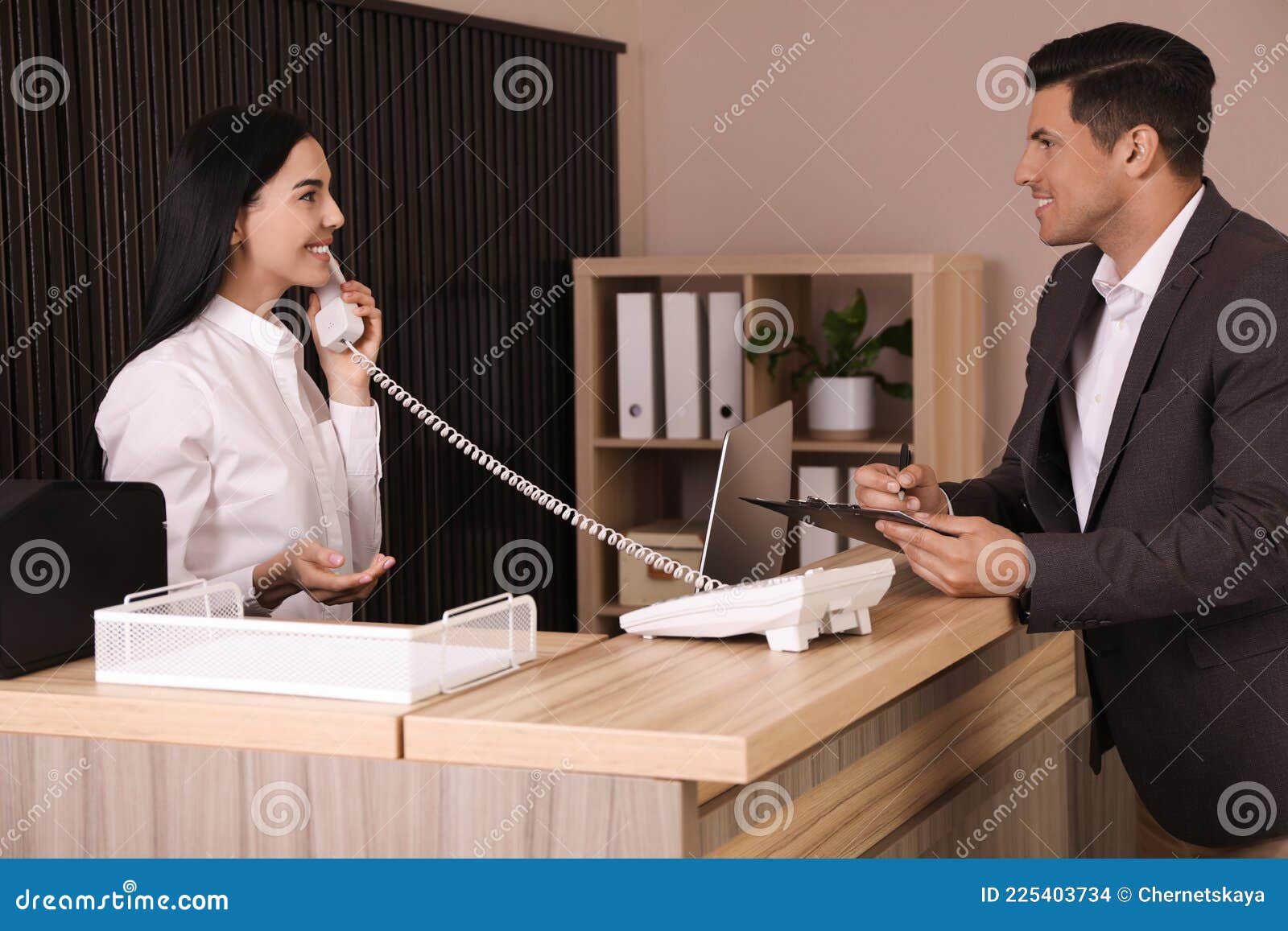 Receptionist Talking on Phone while Working with Client at Countertop ...