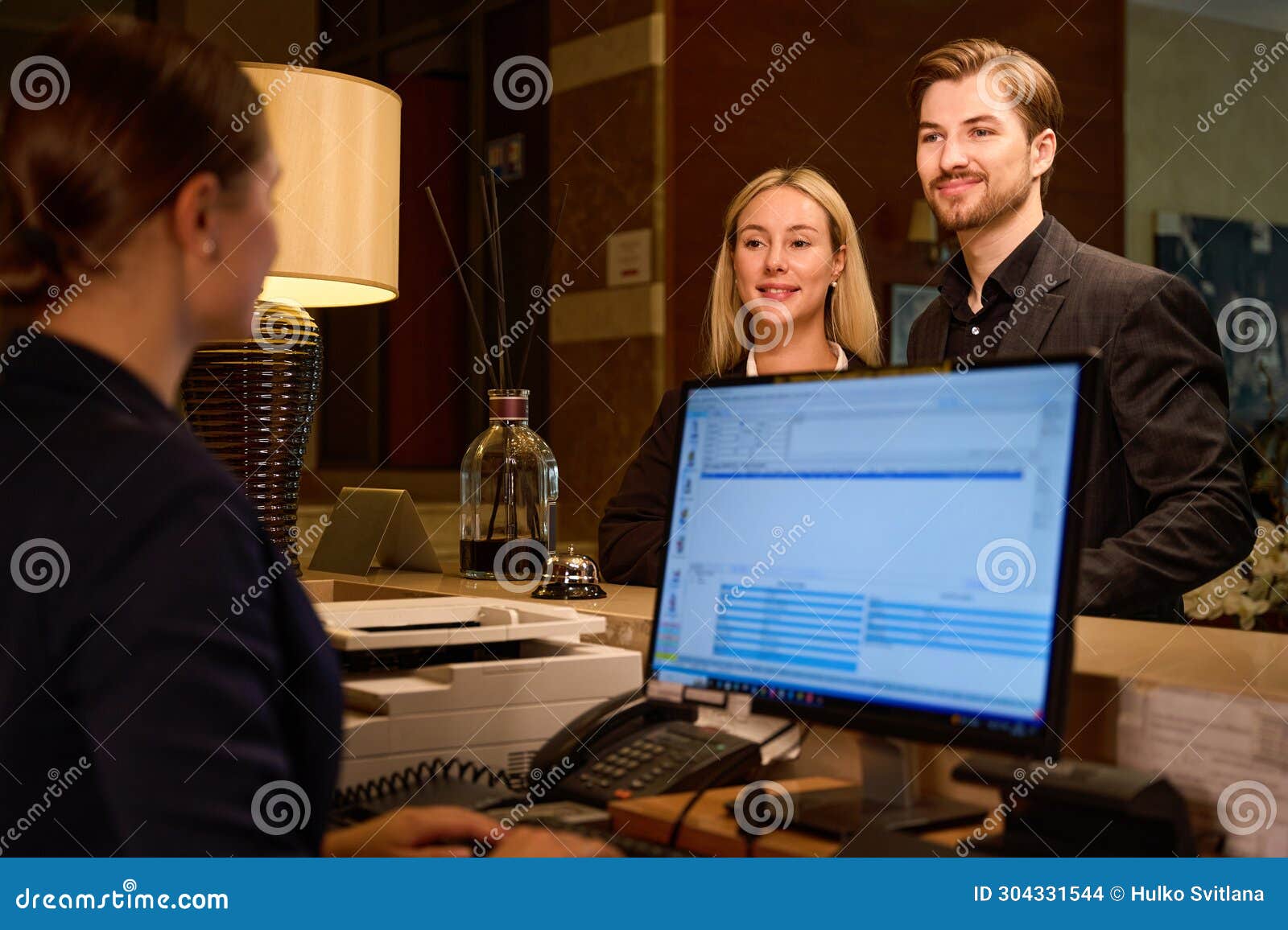 Receptionist Typing on Computer while Couple Standing at Reception Desk ...
